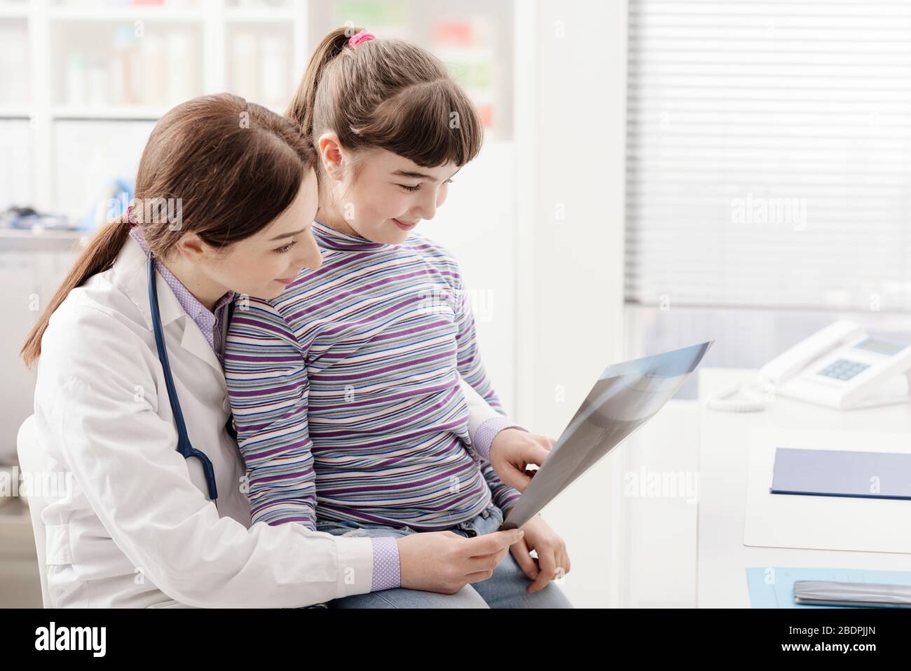 Friendly female doctor showing an x-ray image to a girl, she is holding ...