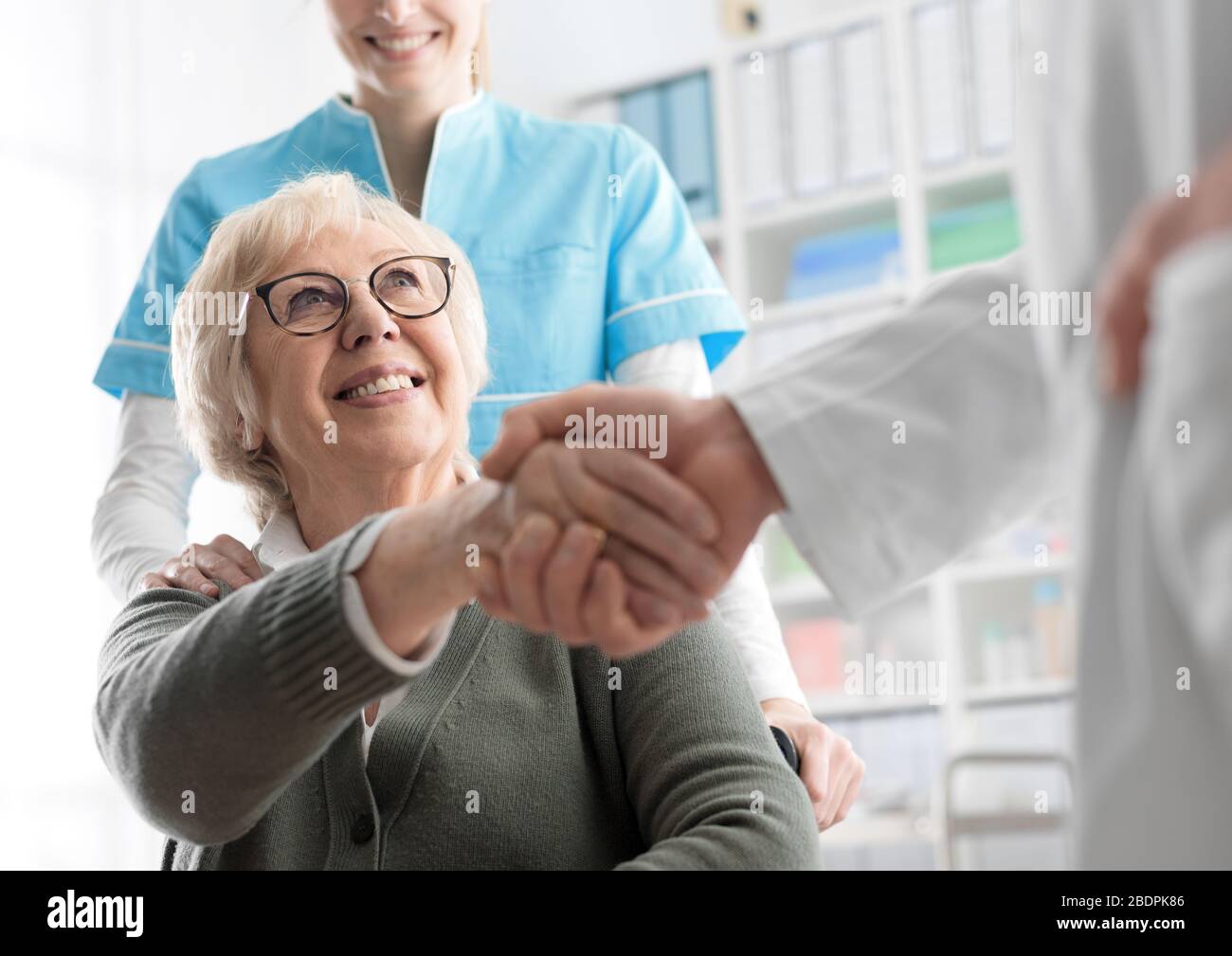 Doctor giving an handshake to a smiling senior female patient and ...