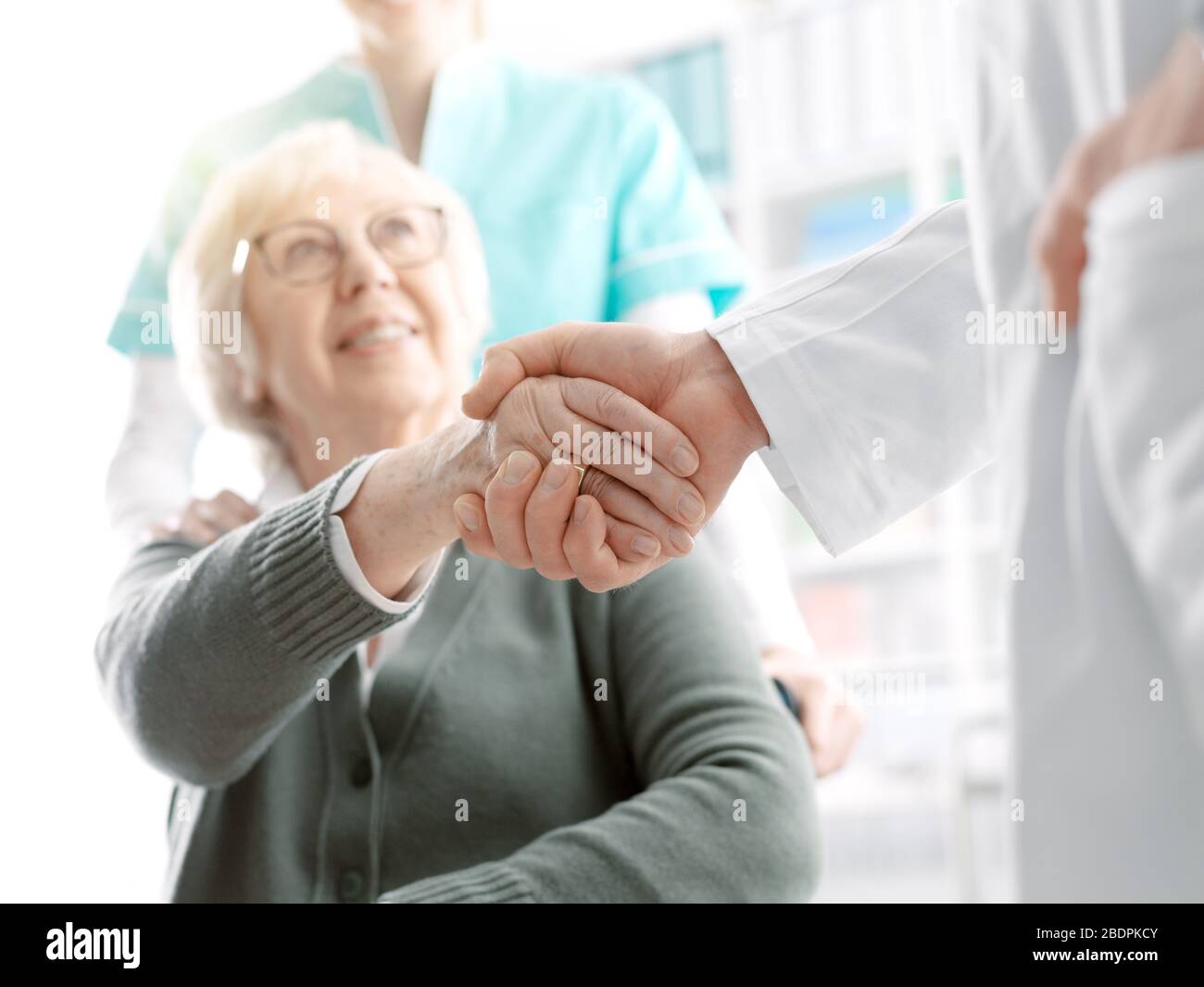 Doctor giving an handshake to a smiling senior female patient and ...