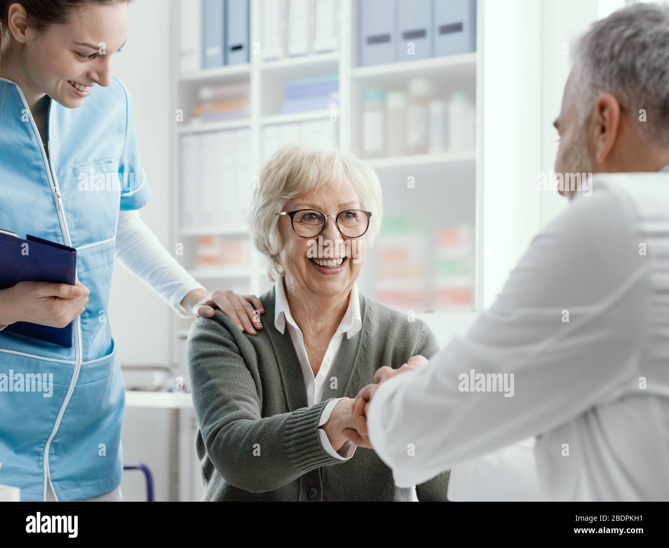 Doctor giving an handshake to a smiling senior female patient and ...