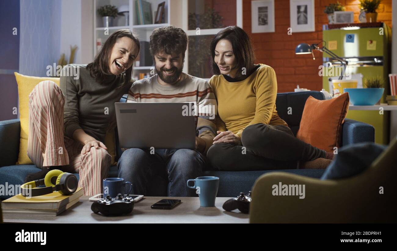 Cheerful friends sitting on the sofa at home and connecting online with ...