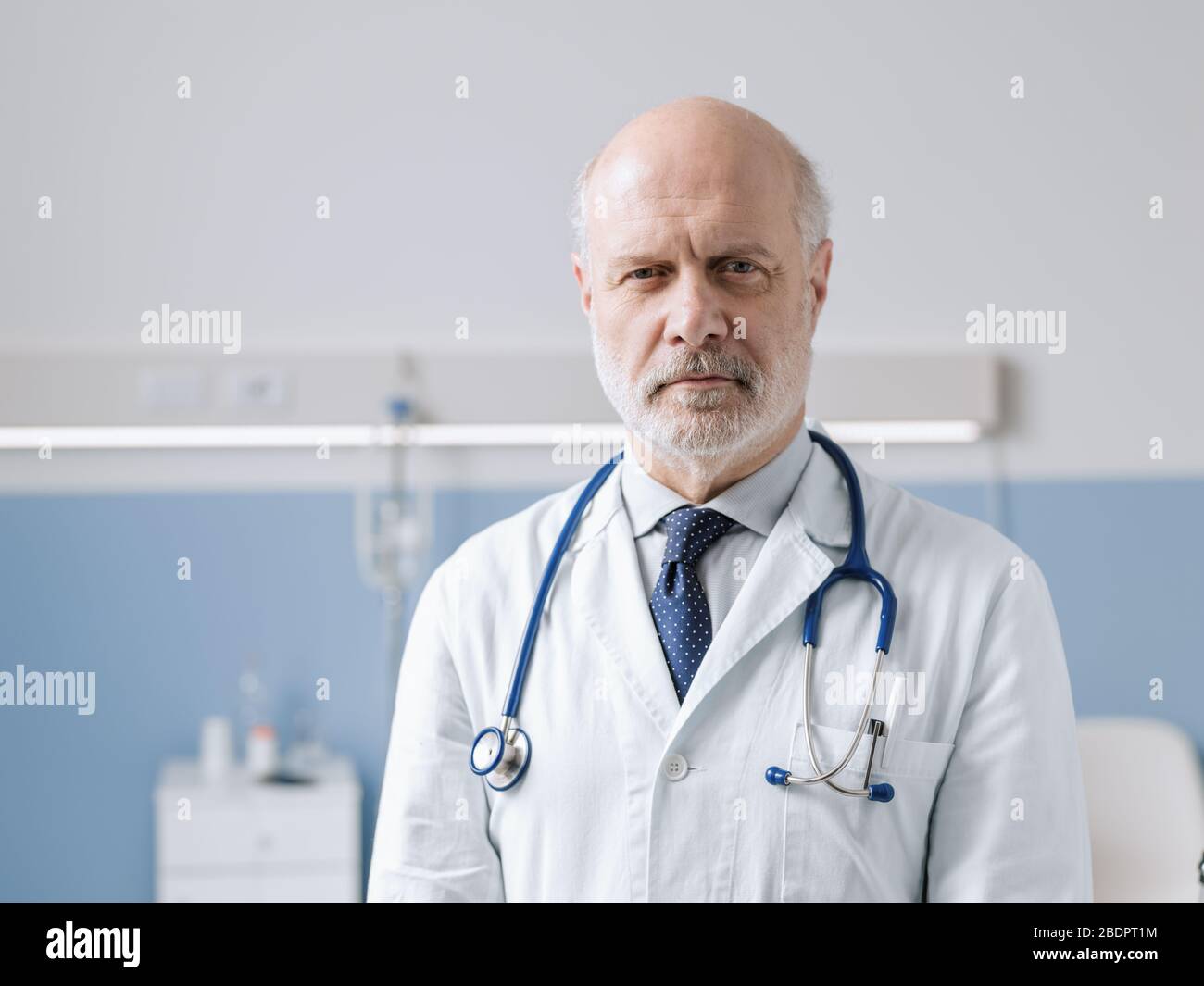 Professional doctor standing next to a hospital bed and looking at ...