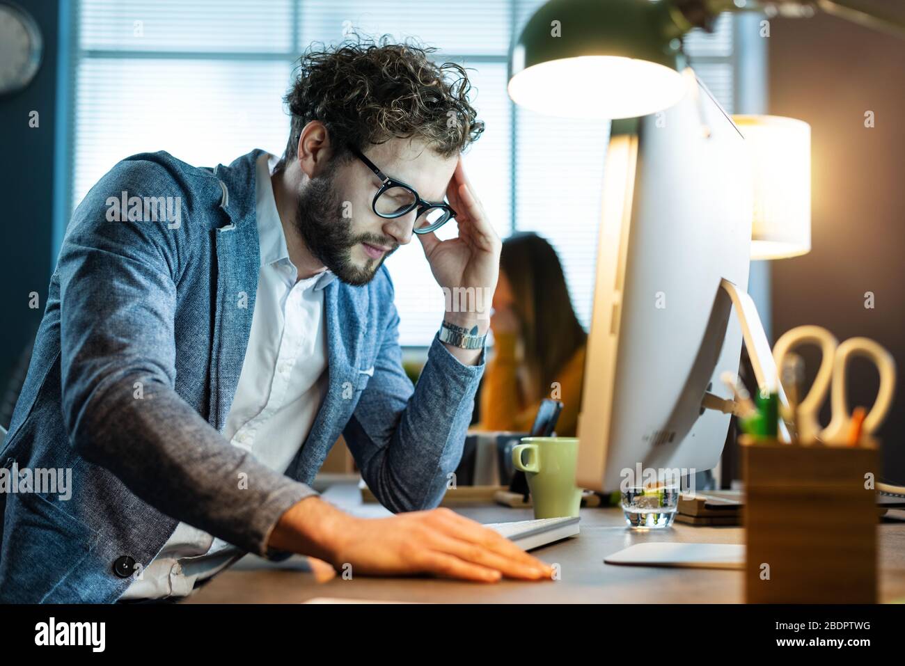 Stressed office worker sitting at desk and working with his computer ...