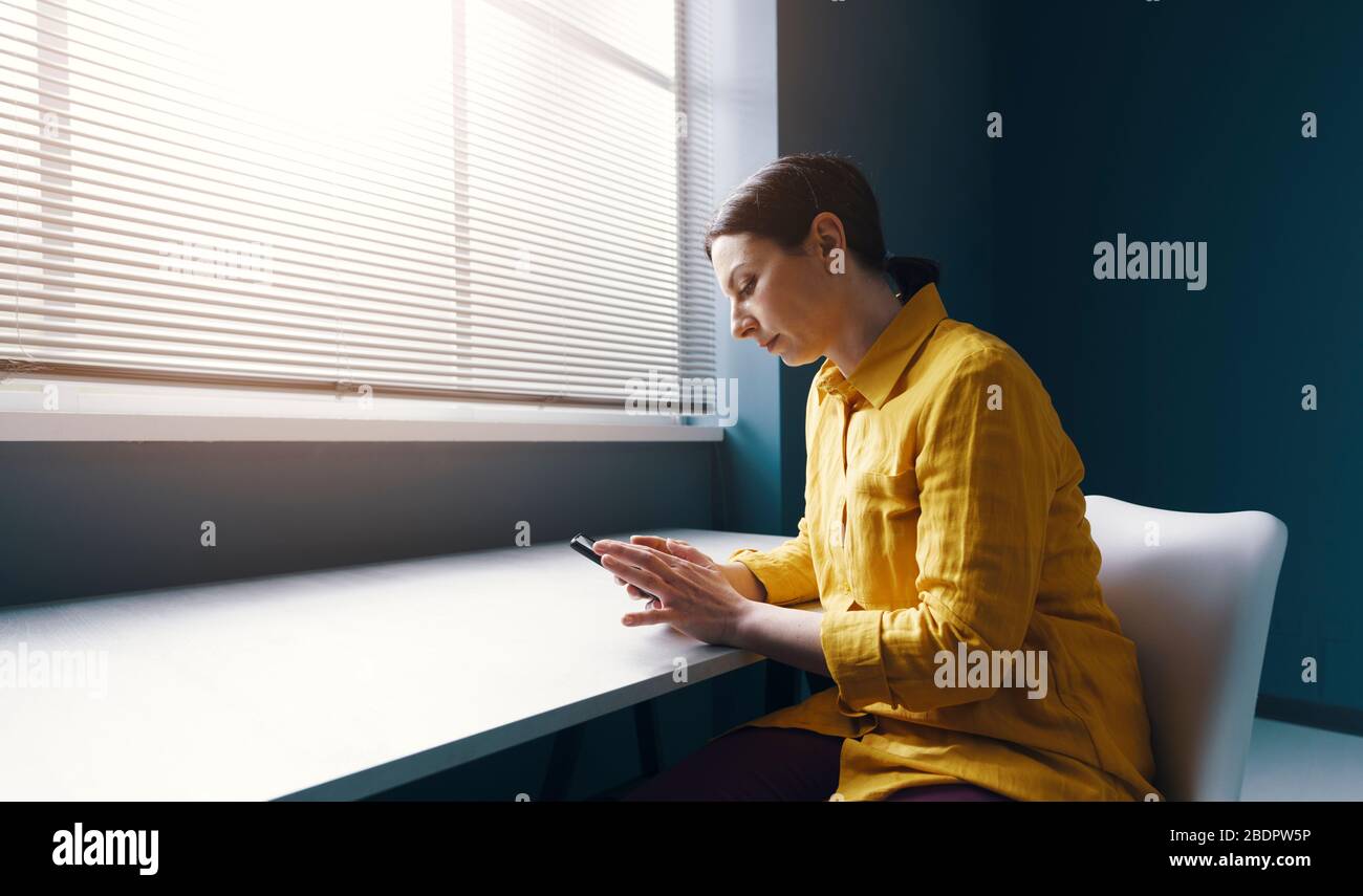 Sad lonely woman isolated at home and chatting with her smartphone ...