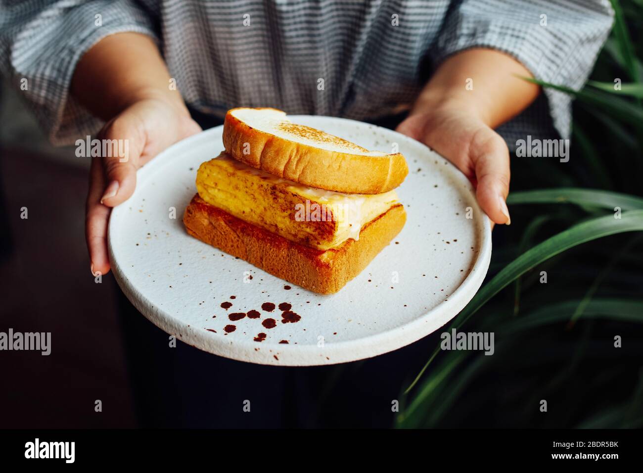 Egg rolled bread sandwich on white plate on white plate handed to you ...
