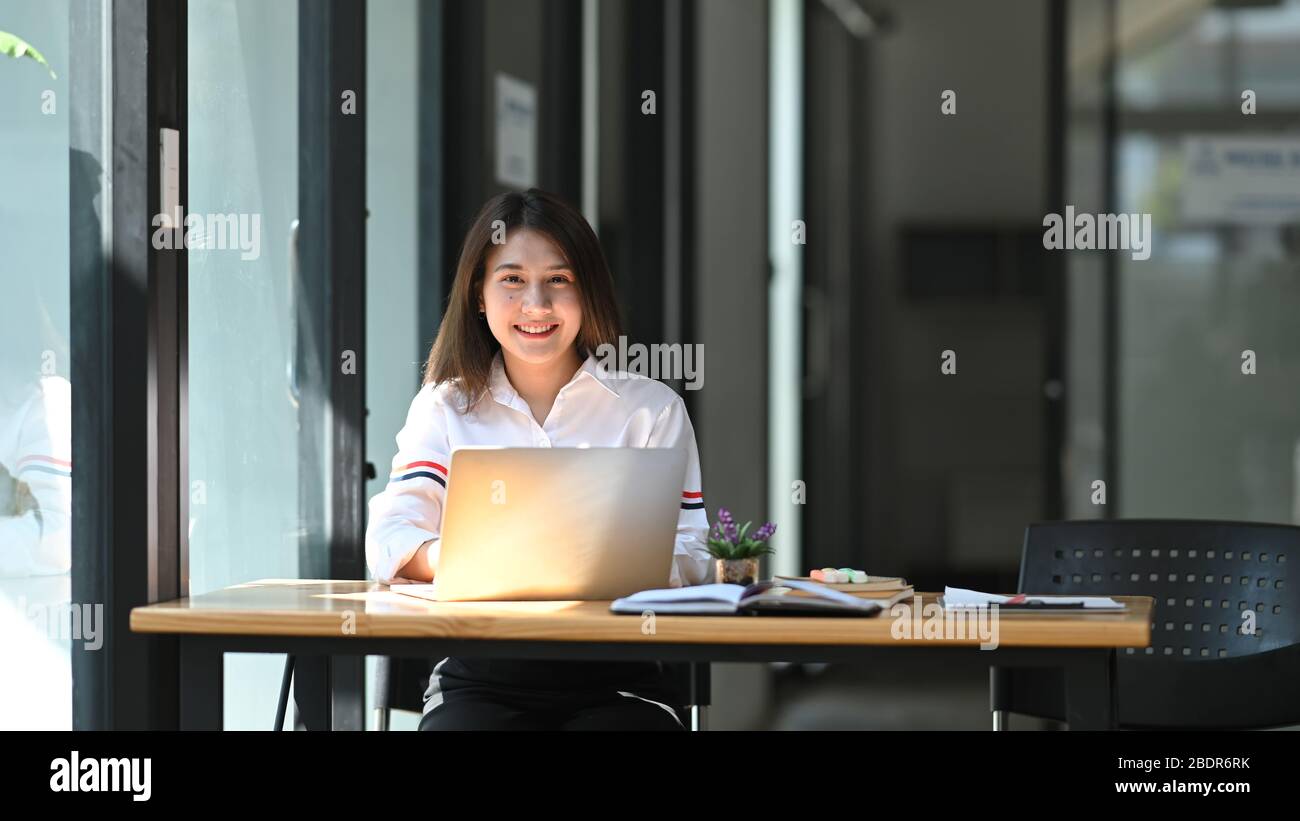 Photo of beautiful girl smiling and sitting in front her computer ...