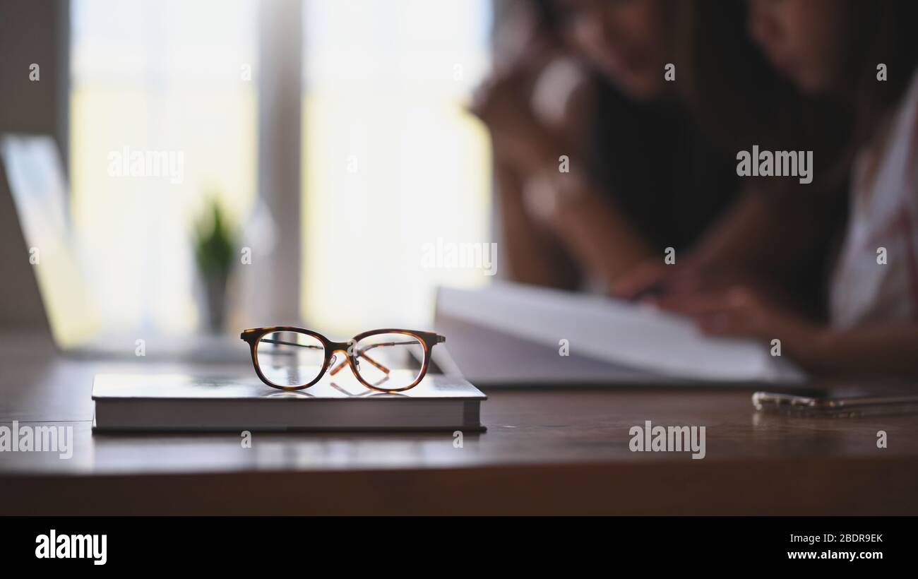 Glasses and book putting together on wooden table with two woman as ...