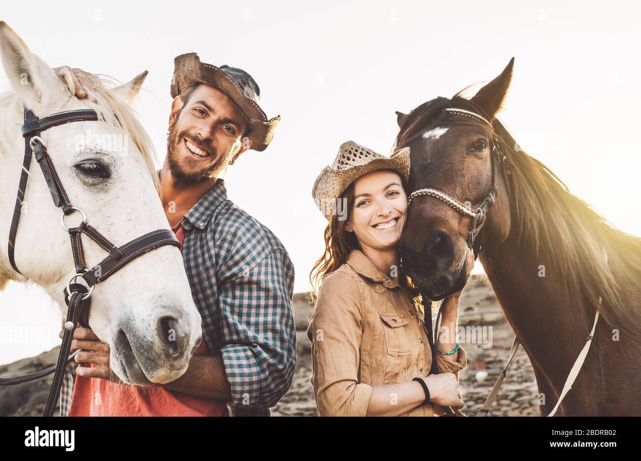 Happy couple having fun with horses inside stable - Young farmers ...