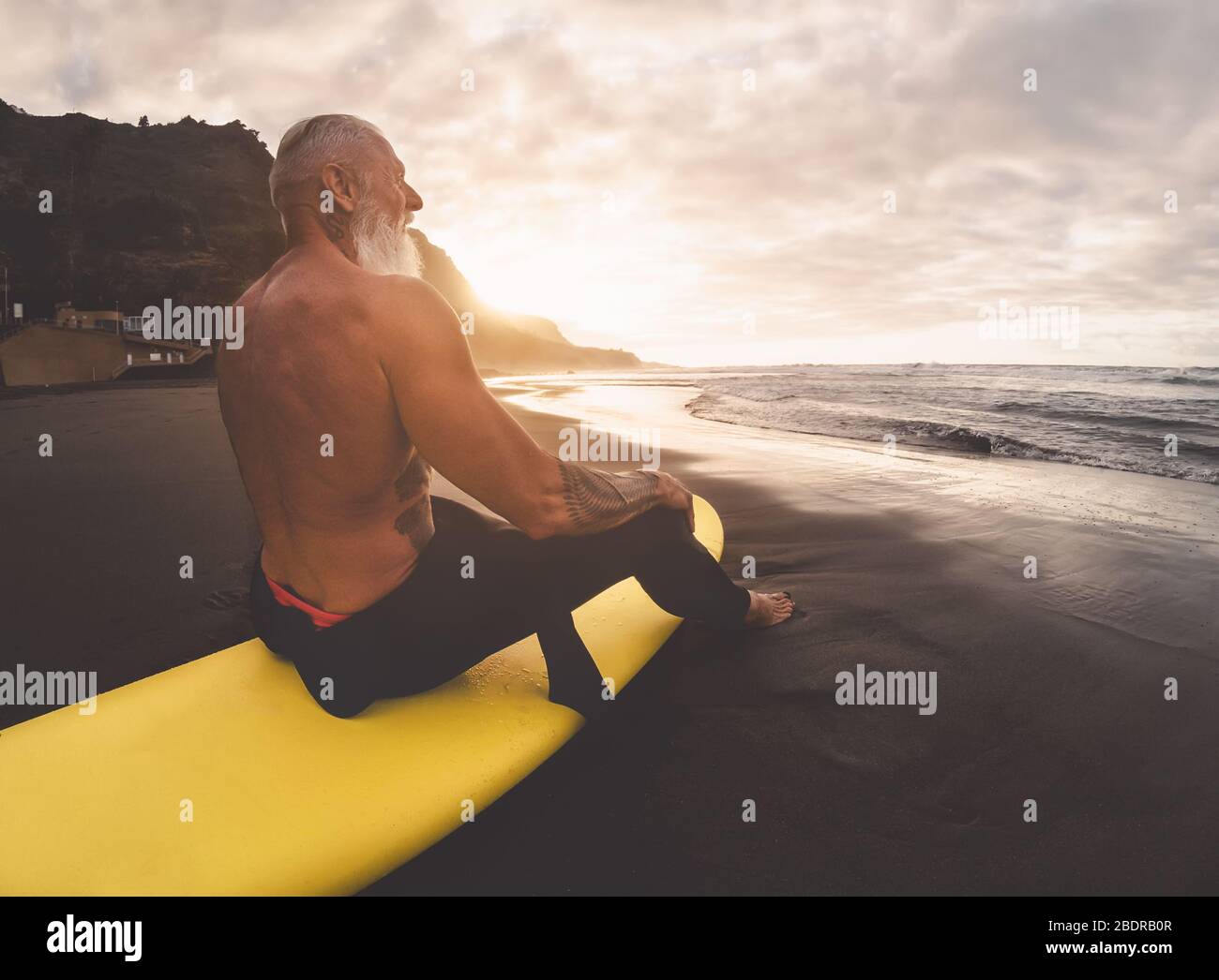 Happy fit senior man sitting on surfboard watching sunset time - Mature ...