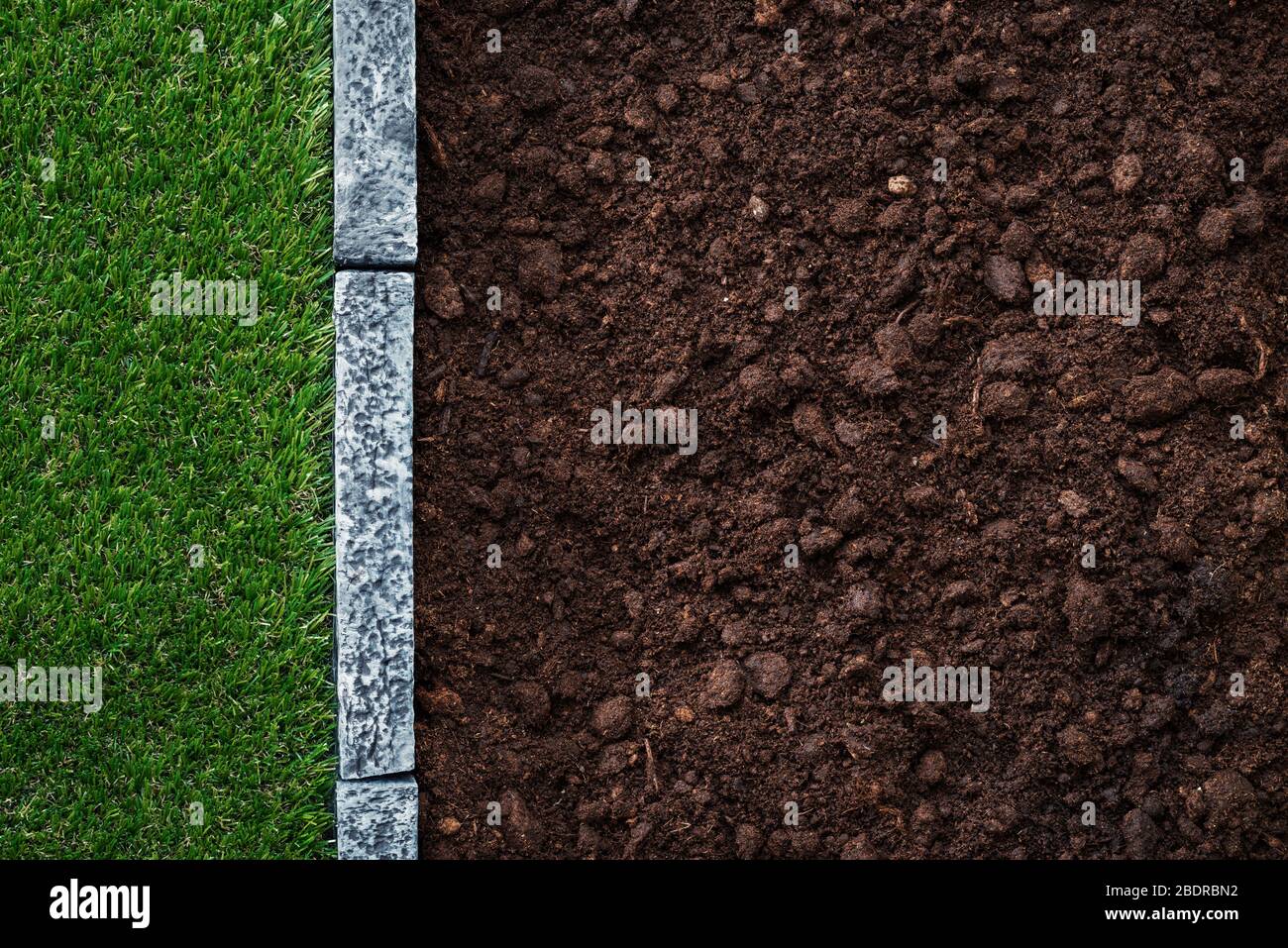 Fertile humus soil and lush grass divided by a stone edging, gardening ...