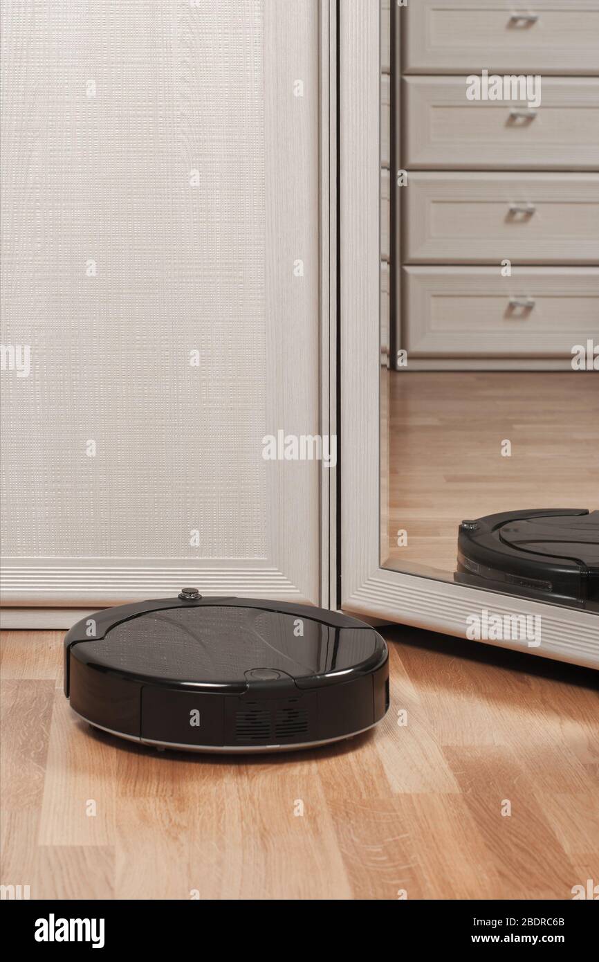 reflection of black robot vacuum cleaner running before mirror in ...