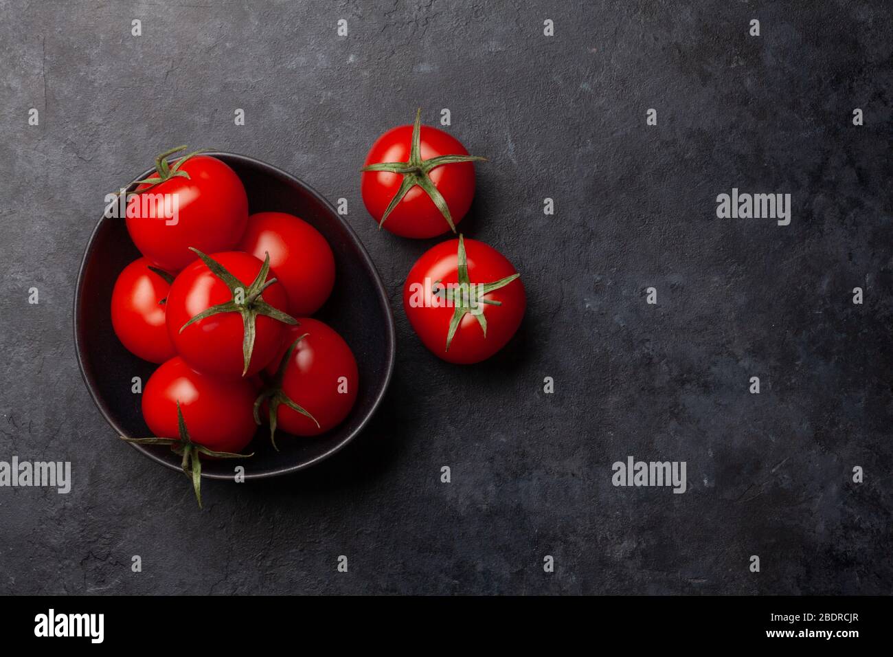 Fresh ripe tomatoes in bowl on stone table. Top view with copy space ...