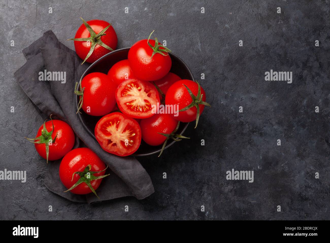 Fresh ripe tomatoes in bowl on stone table. Top view with copy space ...