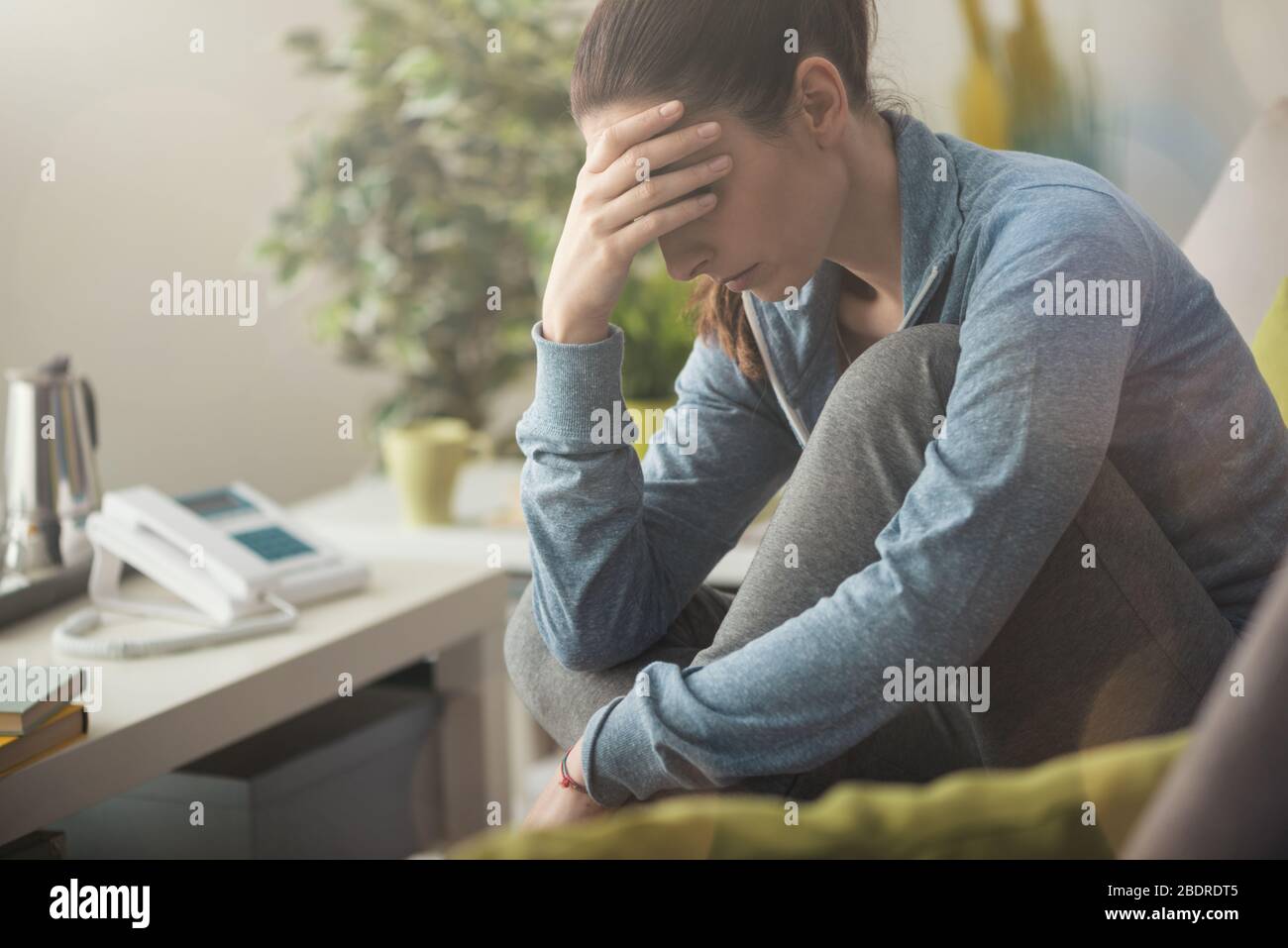 Sad depressed woman at home sitting on the couch, looking down and ...