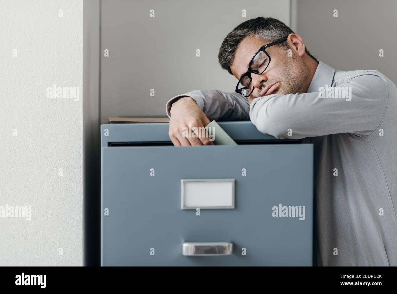 Tired lazy office worker leaning on a filing cabinet and sleeping, he ...