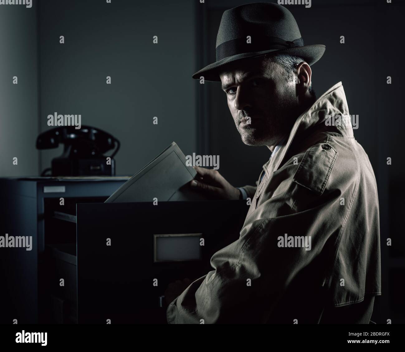 Vintage undercover spy stealing files in a filing cabinet late at night ...