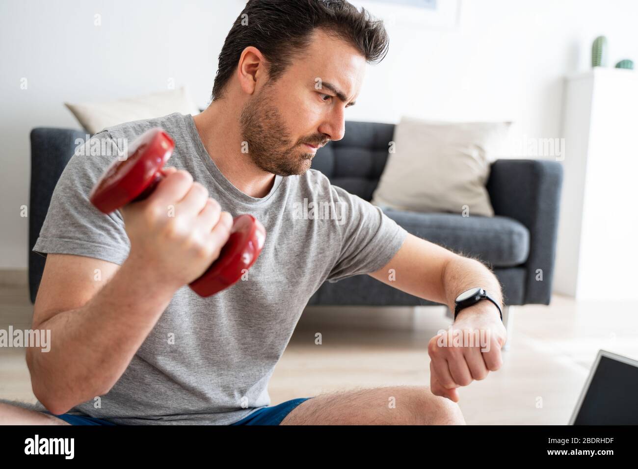 Young active man checking time in smartwatch during home trainings ...