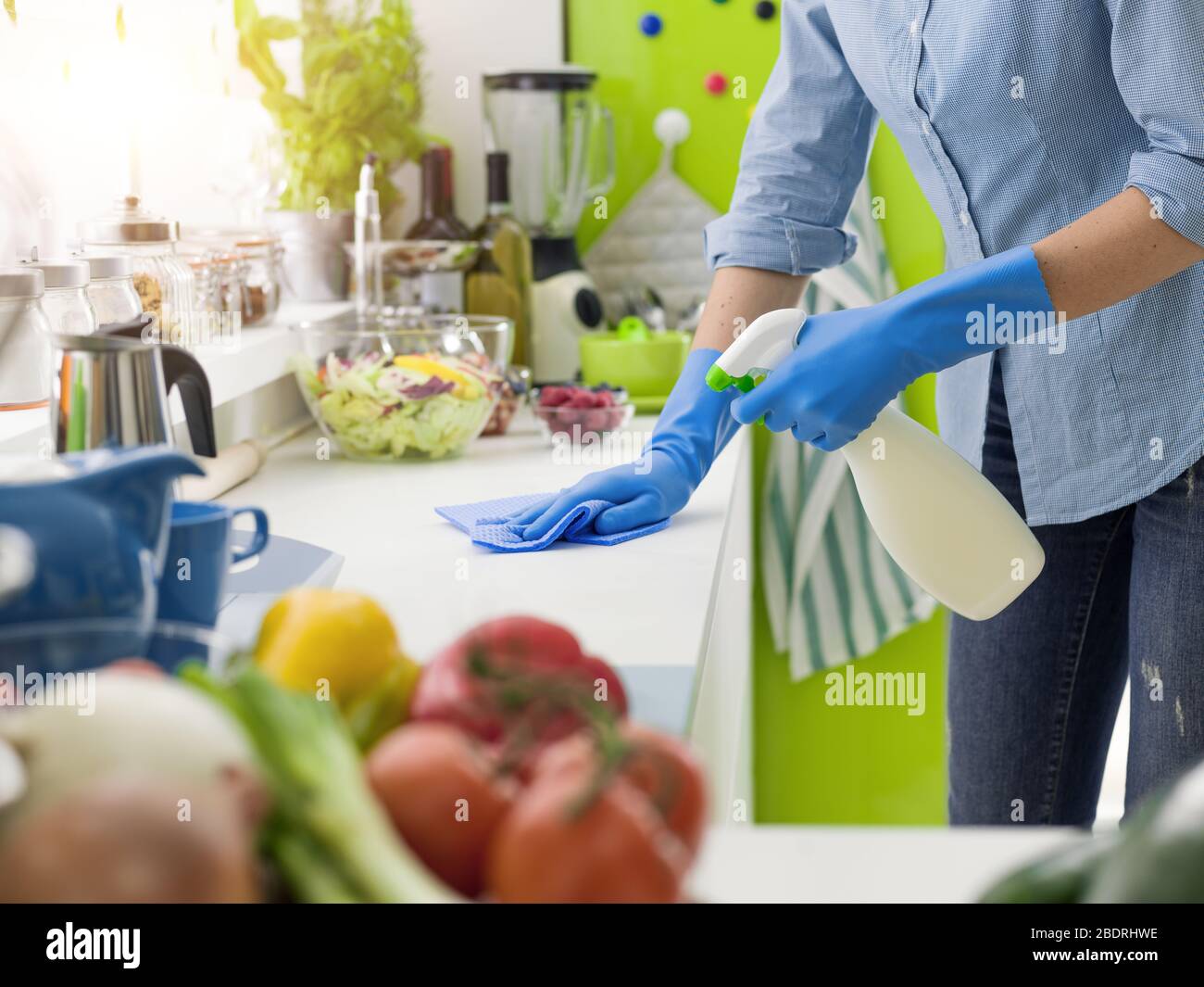 Woman cleaning and polishing the kitchen worktop with a spray detergent ...