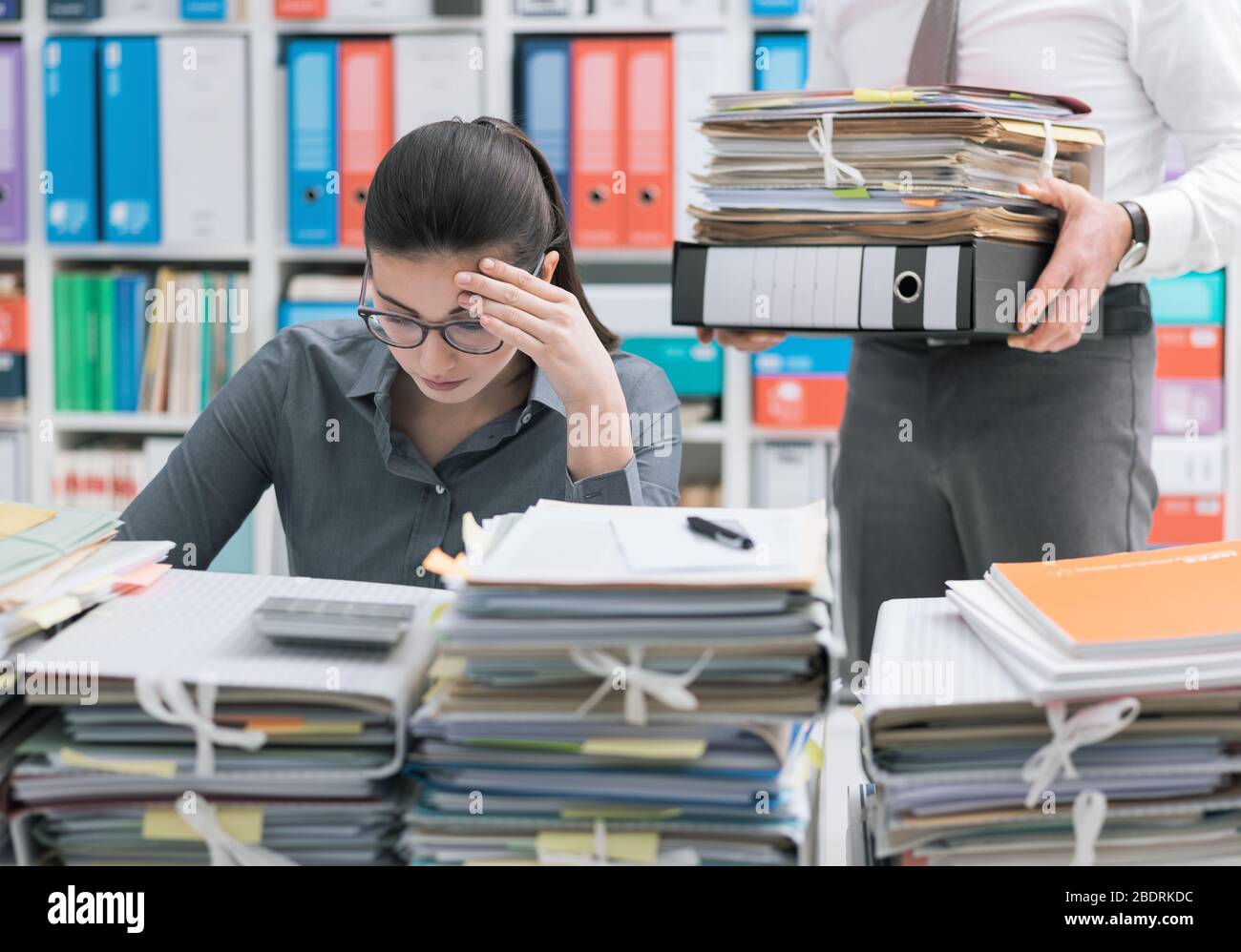 Young stressed secretary in the office overwhelmed by work and desk ...