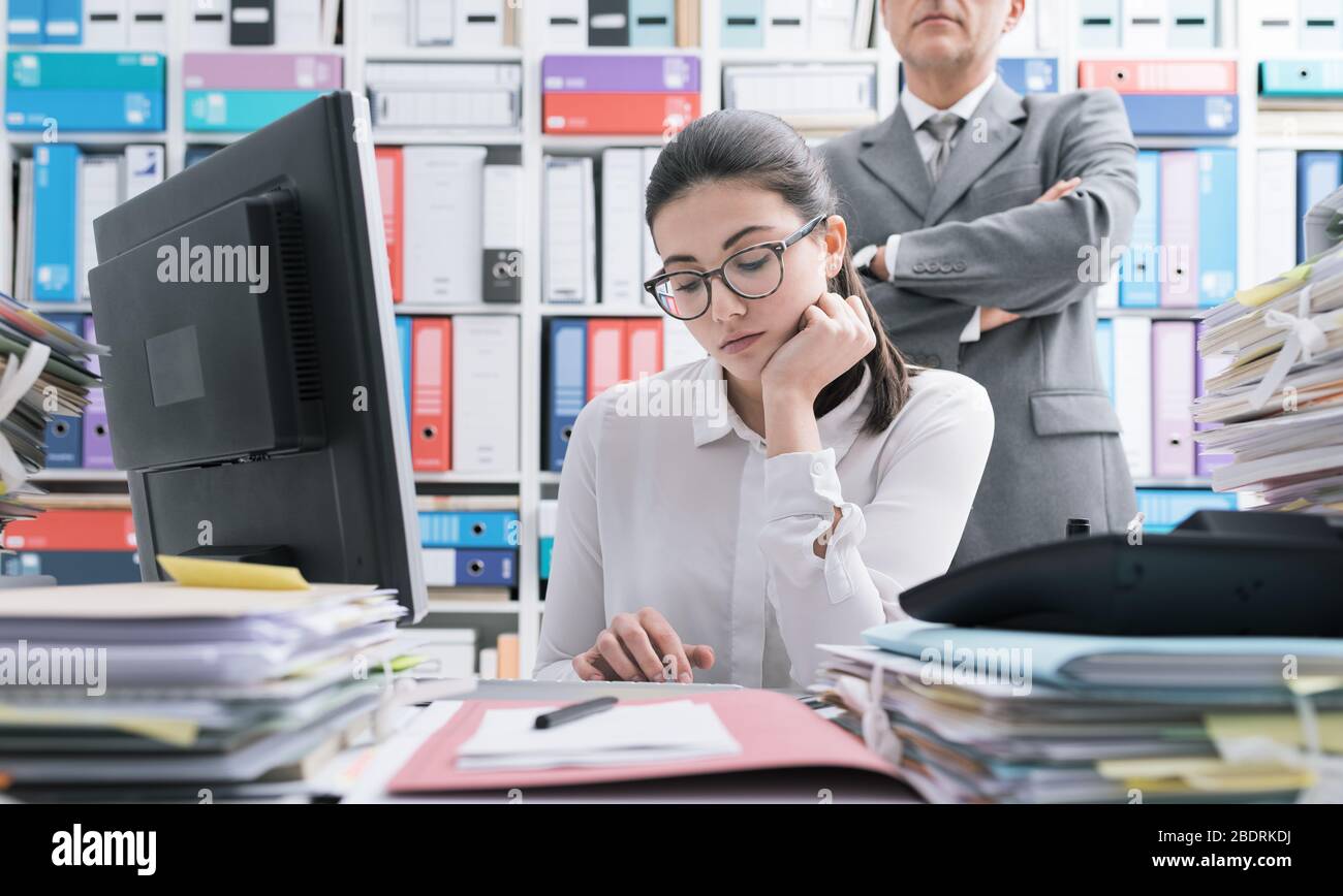 Boss watching over his young employee and standing behind her, she is ...
