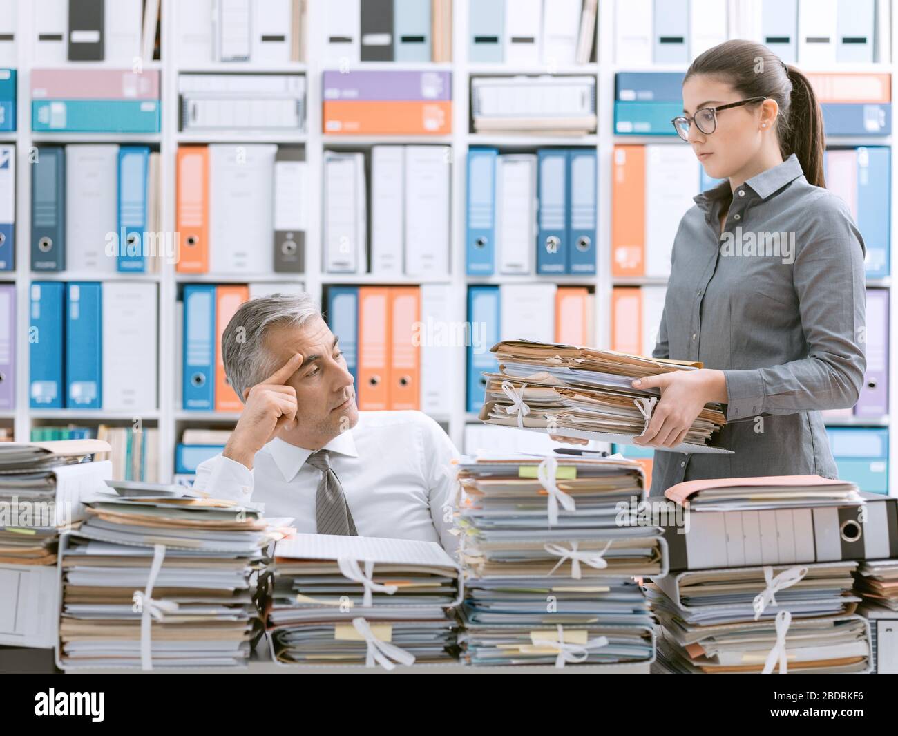 Stressed businessman working at office desk and overloaded with work ...