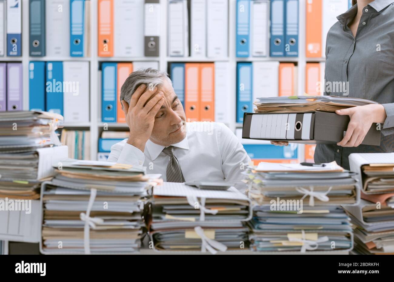 Stressed businessman working at office desk and overloaded with work ...