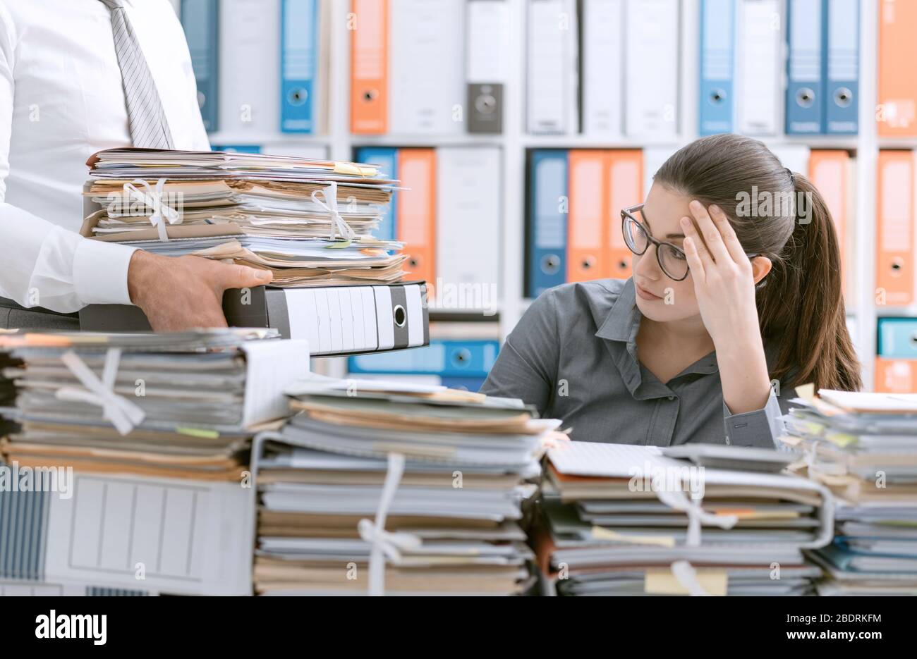 Young stressed secretary in the office overwhelmed by work and desk ...