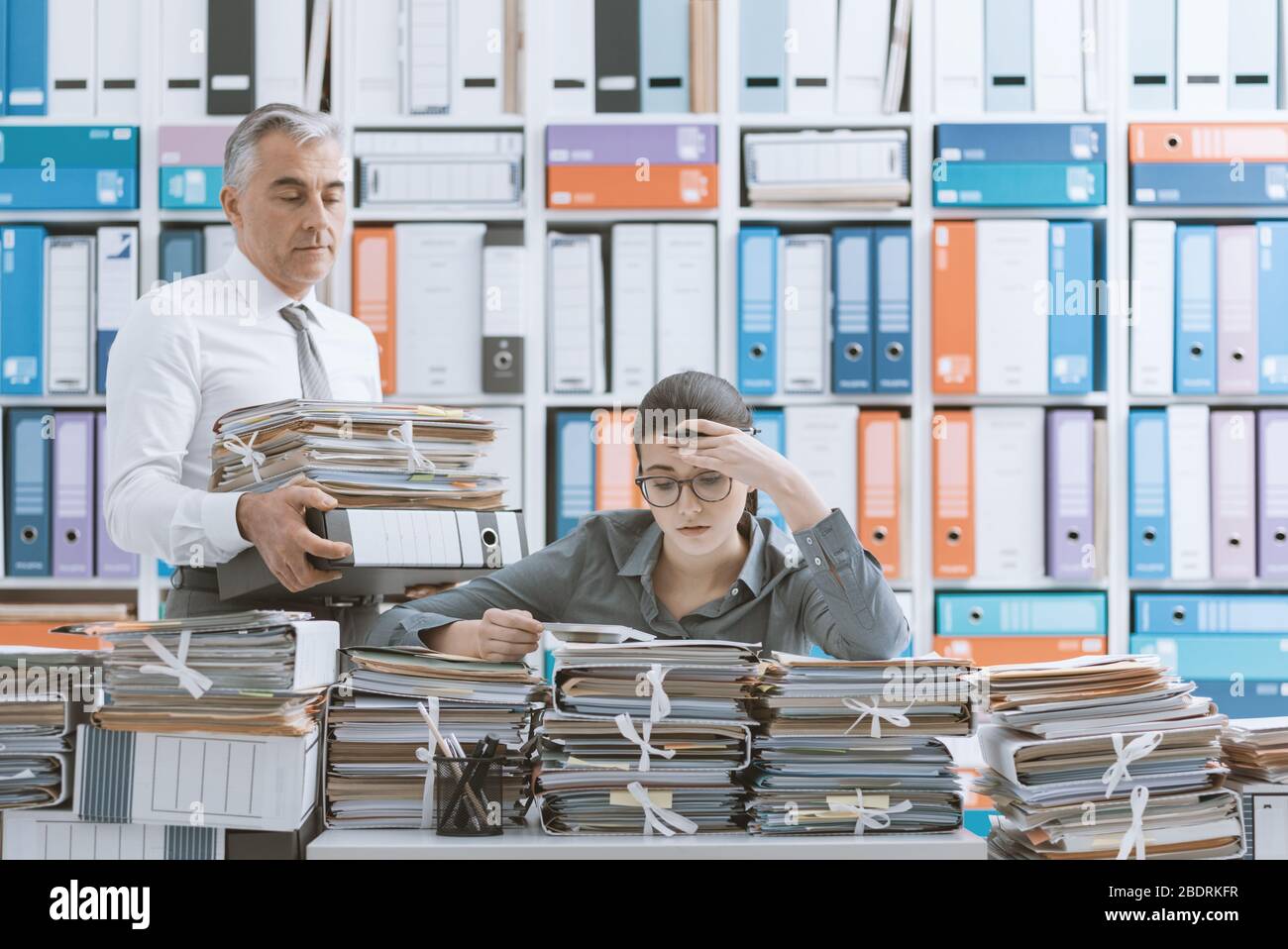 Young stressed secretary in the office overwhelmed by work and desk ...