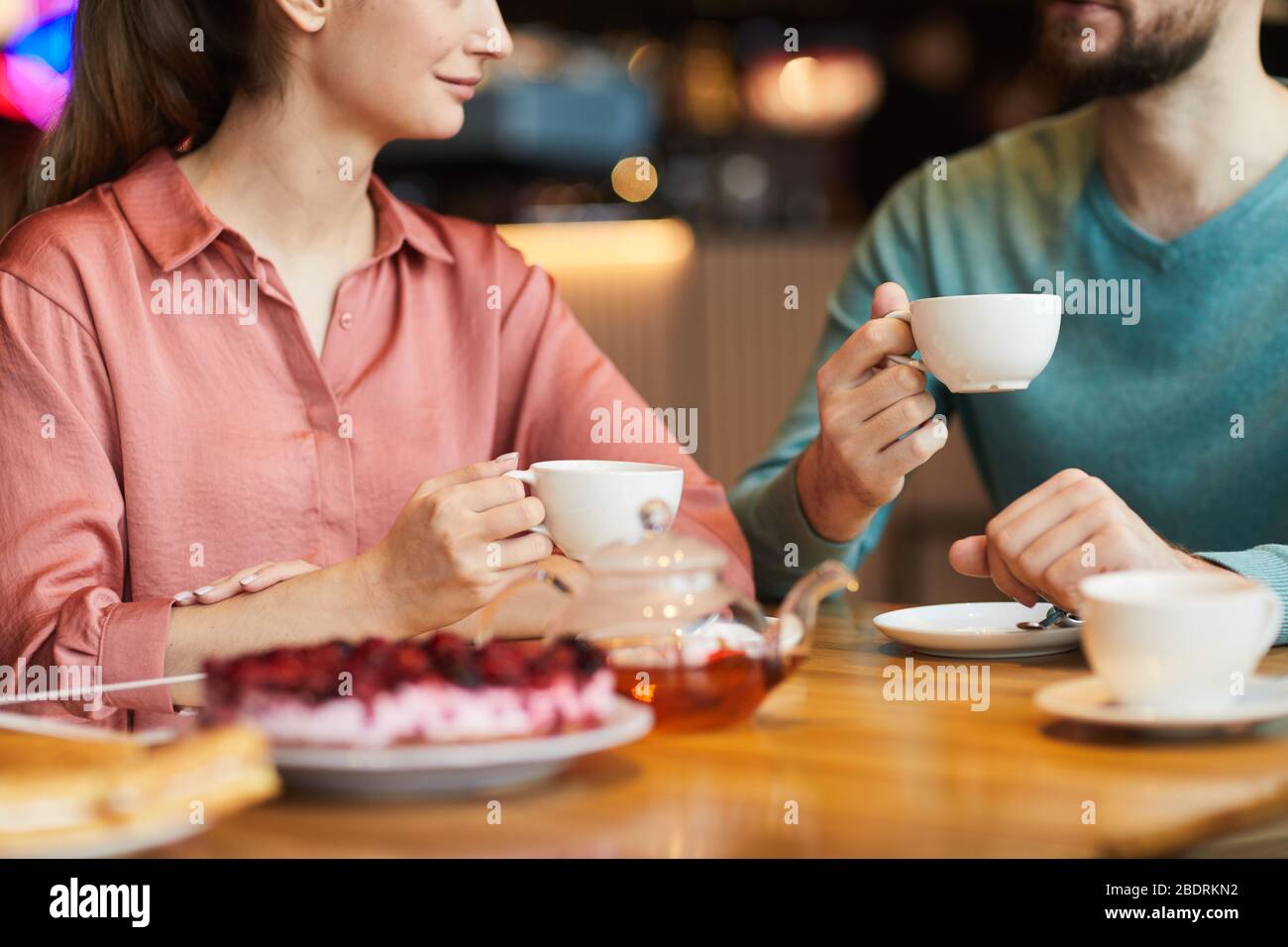 Close-up of young couple sitting at the table drinking tea with pie and ...