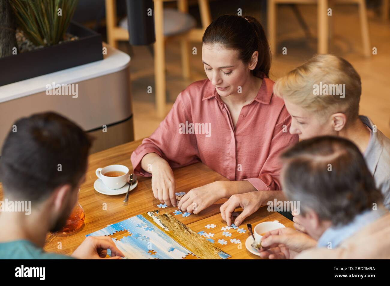 Family of four sitting at the table and collecting puzzle together ...
