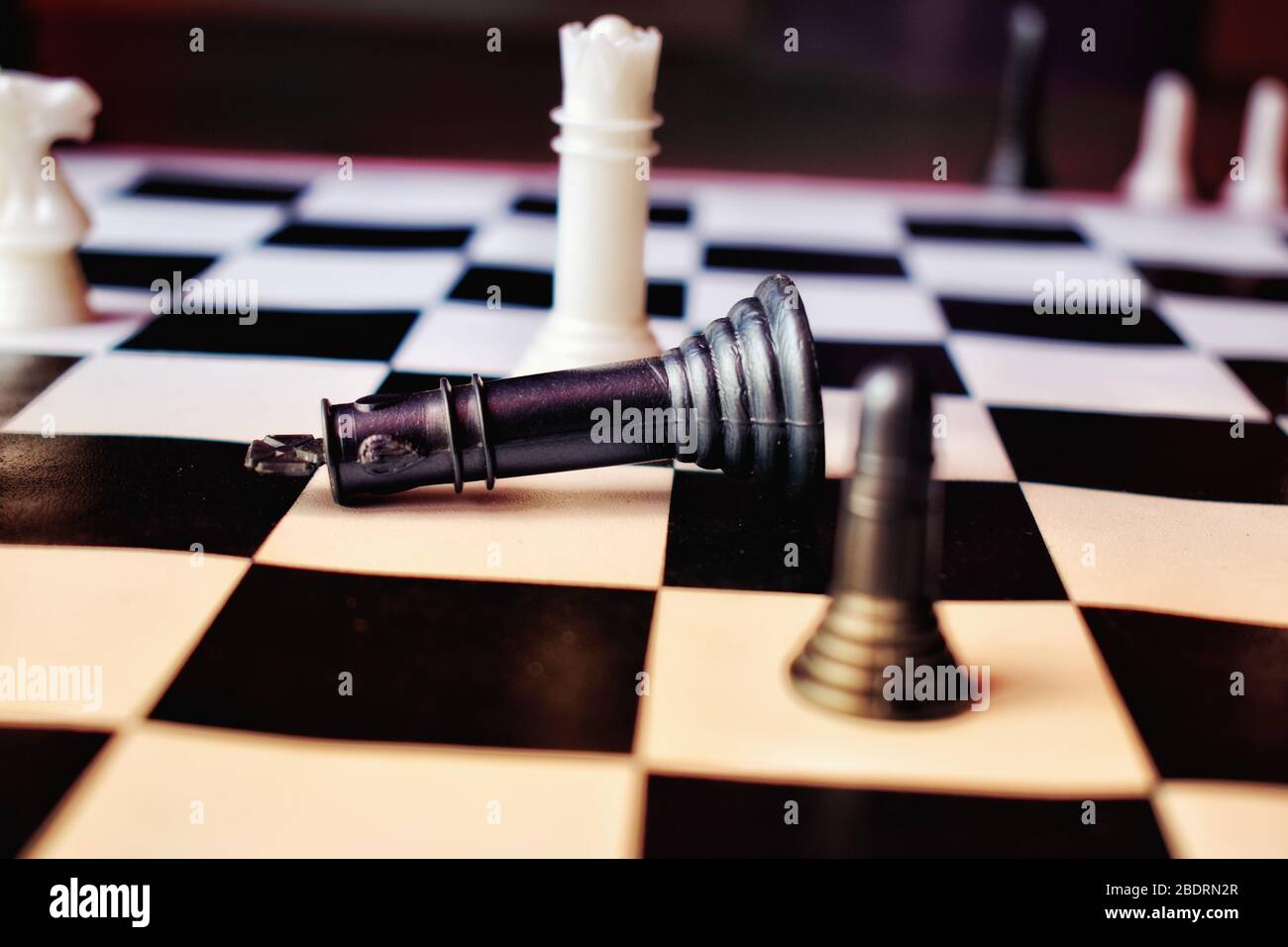 Chess game ongoing on a chess board . the black king fall down on the ...