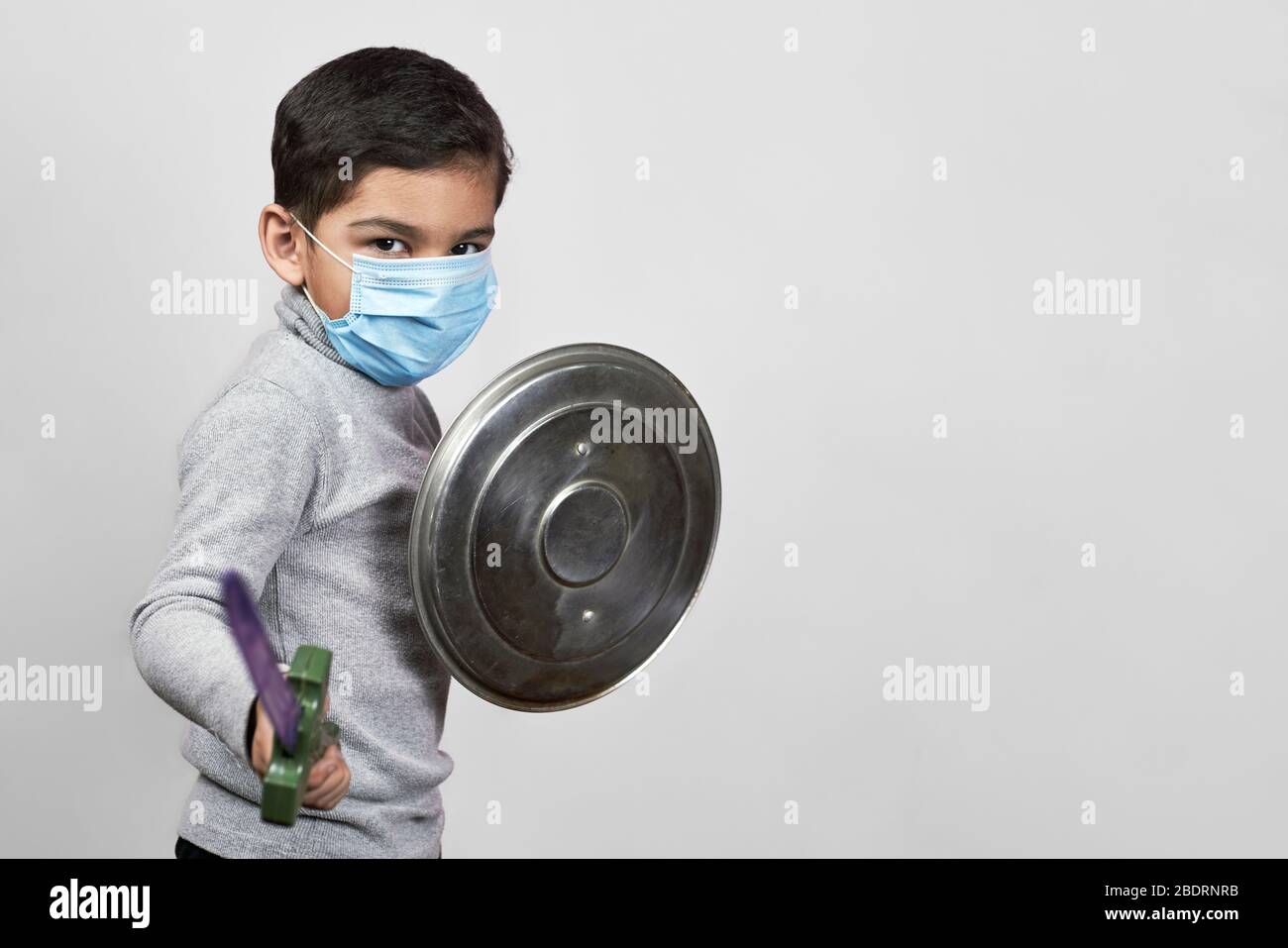 Bored boy in medical face mask plays knight cavalier. Little moddle ...