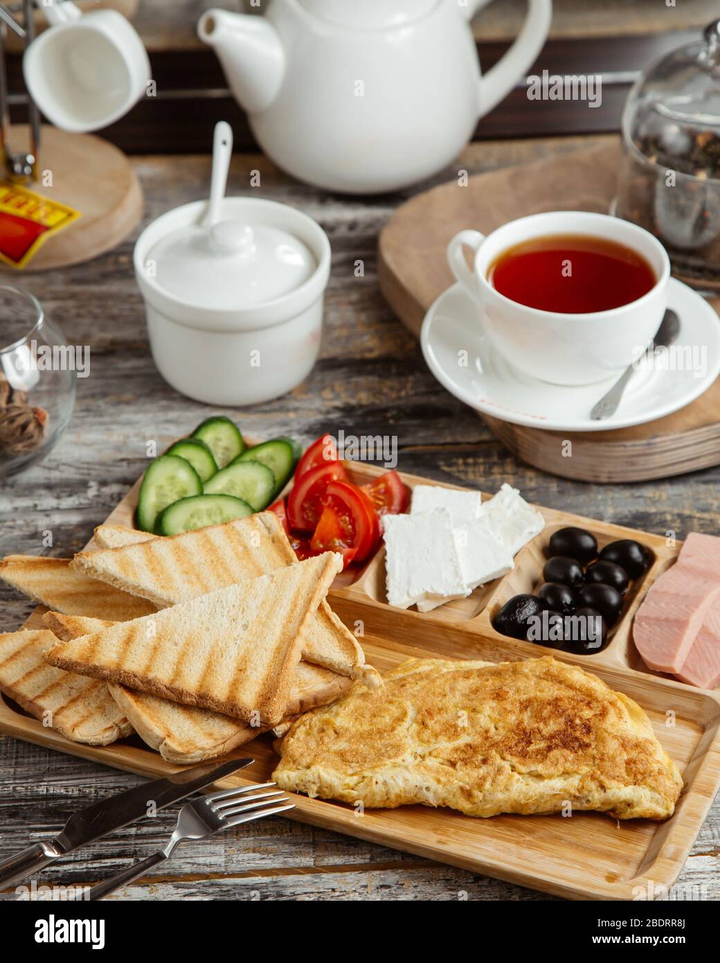breakfast setup with omelet toast cucumber tomato cheese olive and tea ...