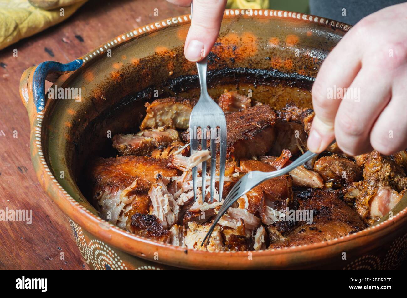 Mexican carnitas. Male hands shredding slow cooked pork carnitas, in the style of Michoacan ...