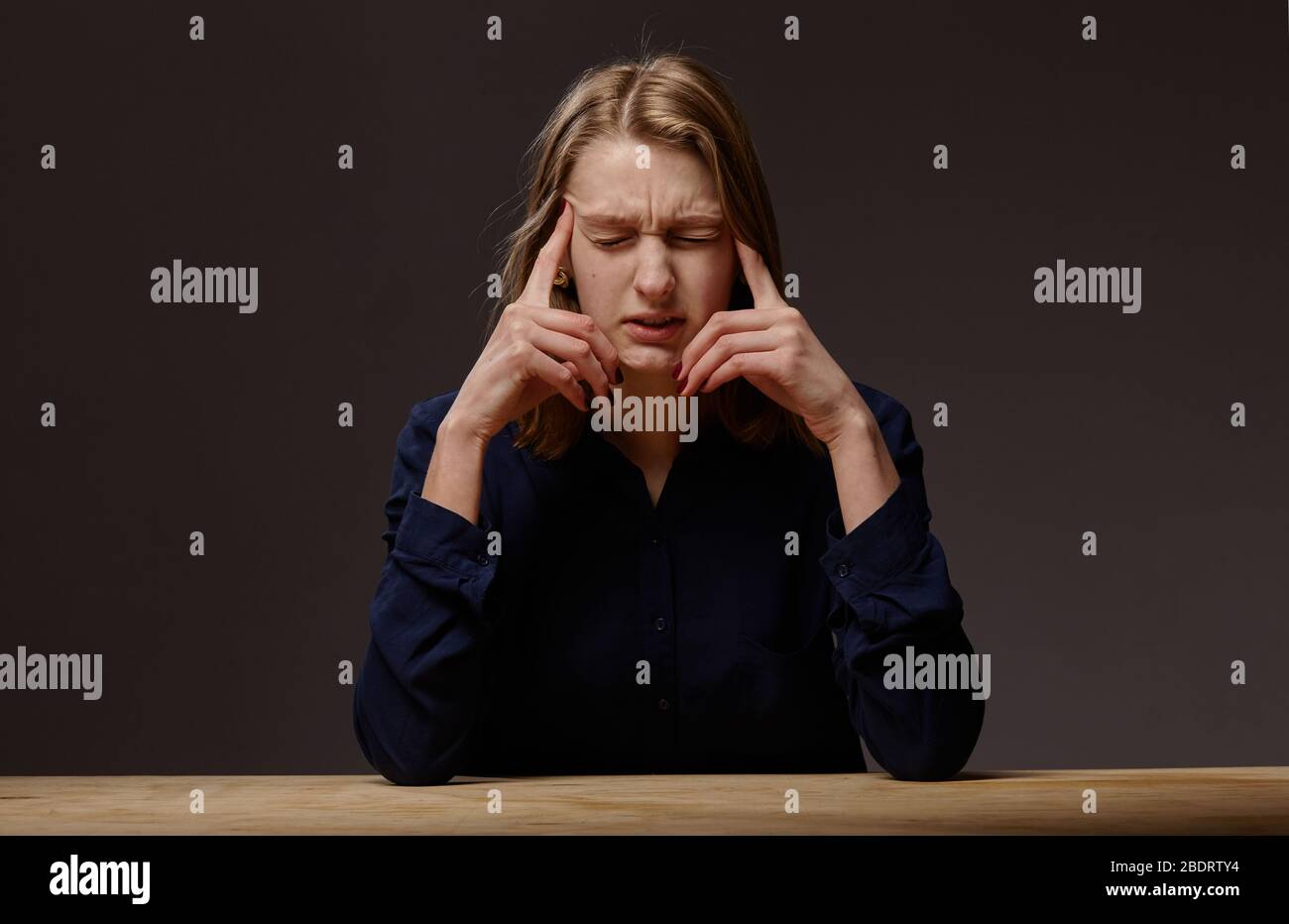 very tense young woman at the table on a dark background Stock Photo ...