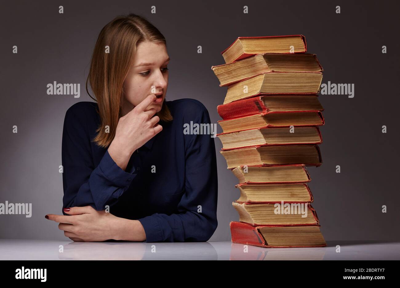 young girl and a lot of books next to her. she has a hard time learning ...