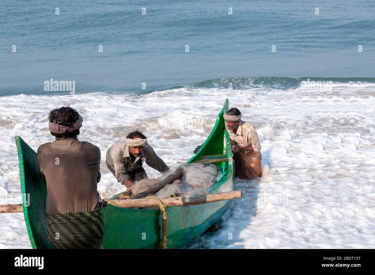 Fishermen hauling their traditional wooden boat from the sea on Marari ...