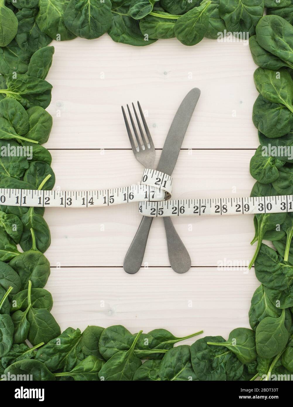 Fresh spinach leaf frame, cutlery and white measure tape on wooden ...