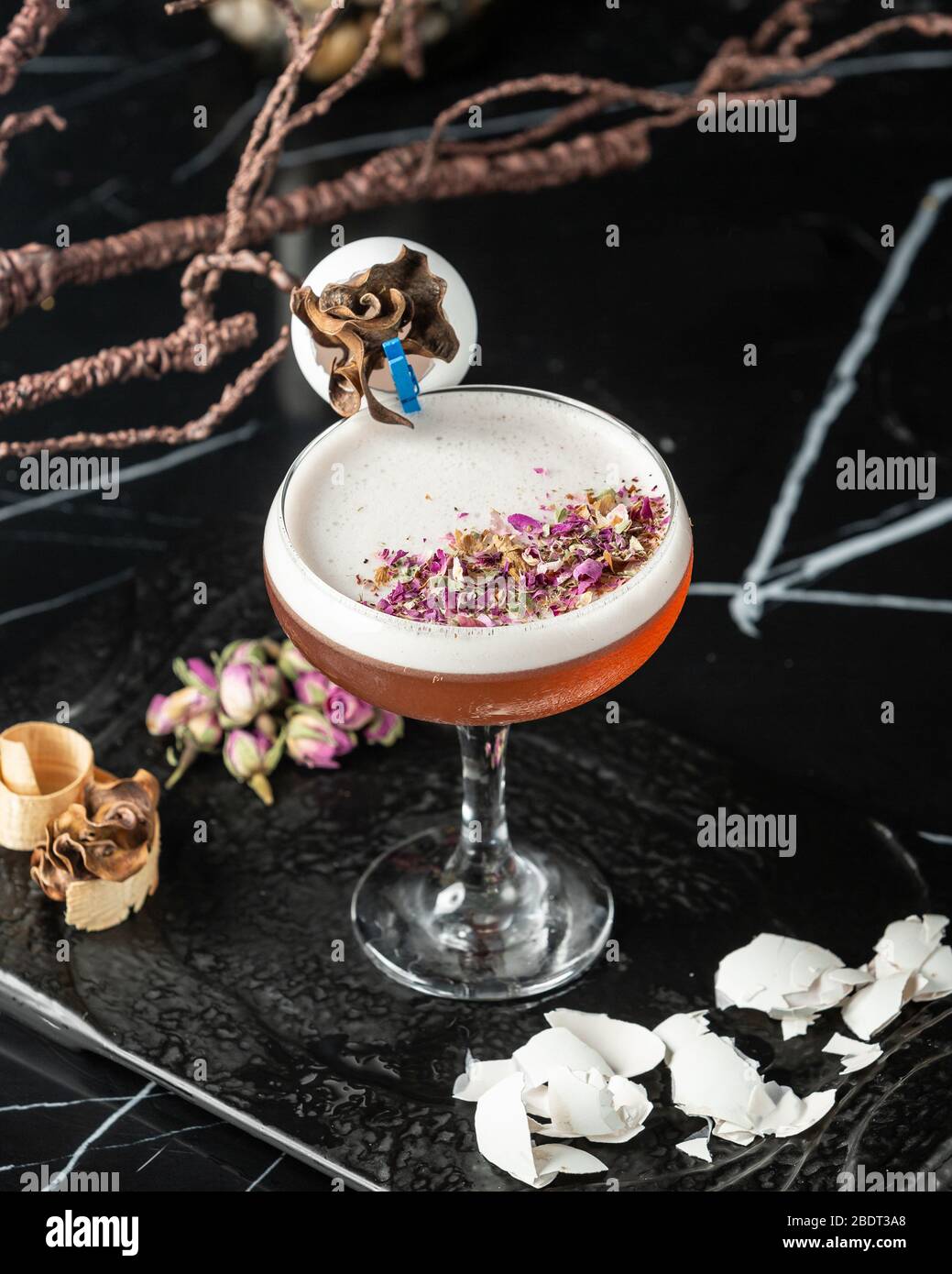 top view of foamy cocktail garnished with rose petal pieces and egg ...