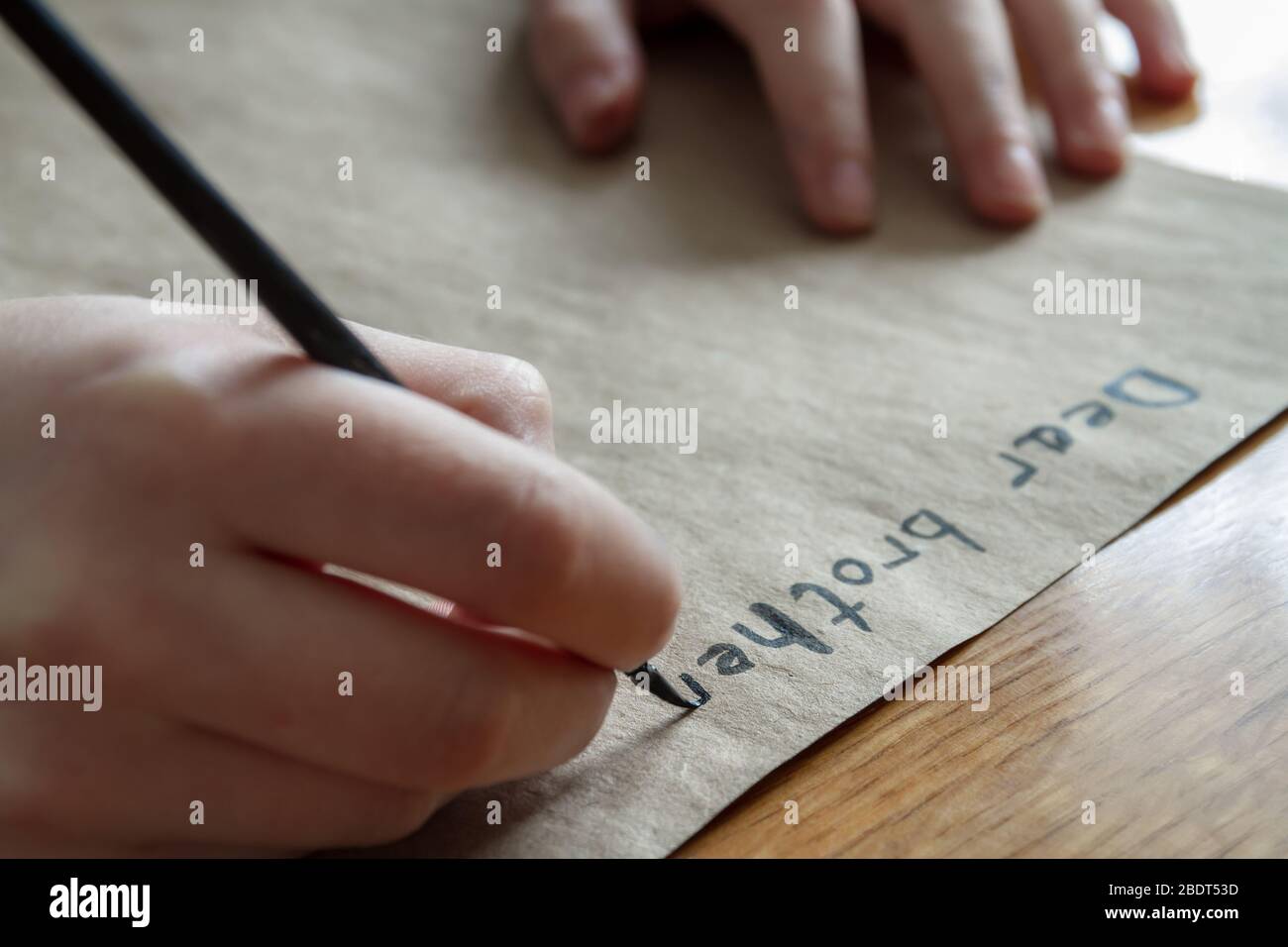 A small girl writes a letter to dear brother by black paint on brown ...