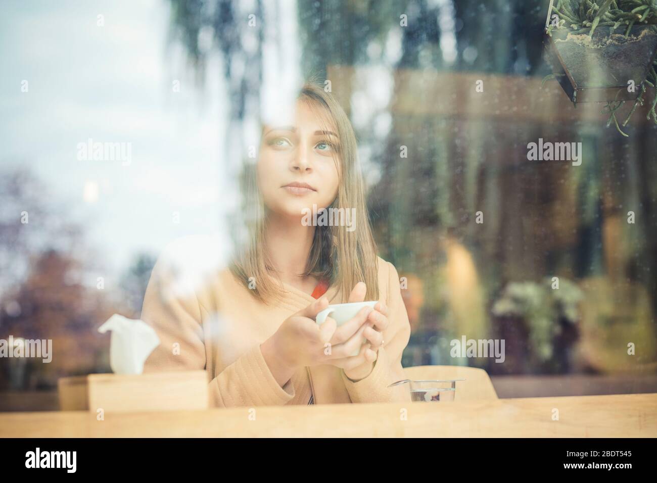 Sad woman alone in a lonely bar after a break up thinking with a rainy ...