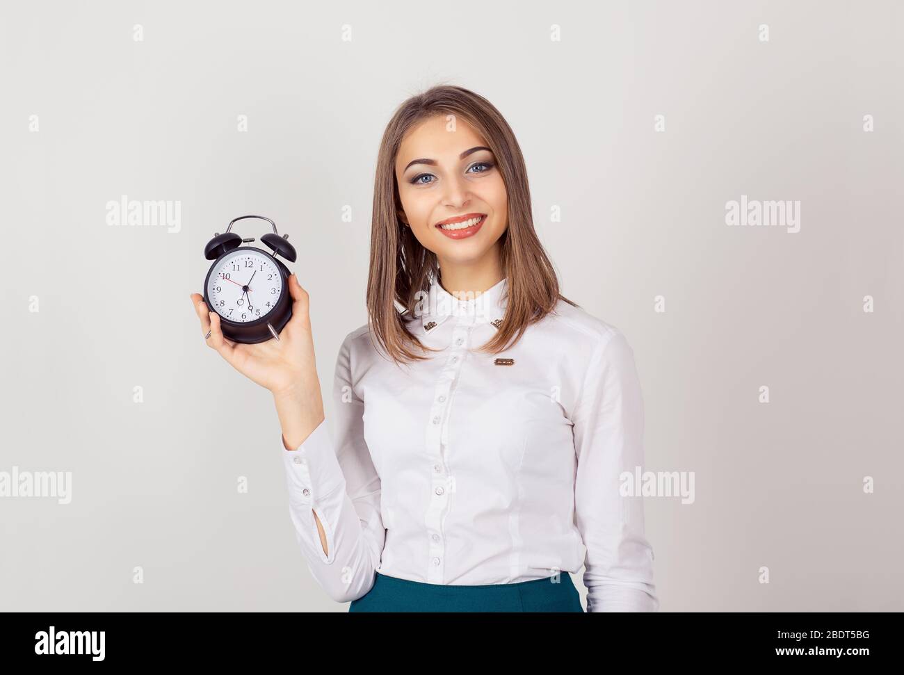 young smiling woman with alarm clock isolated white grey wall ...