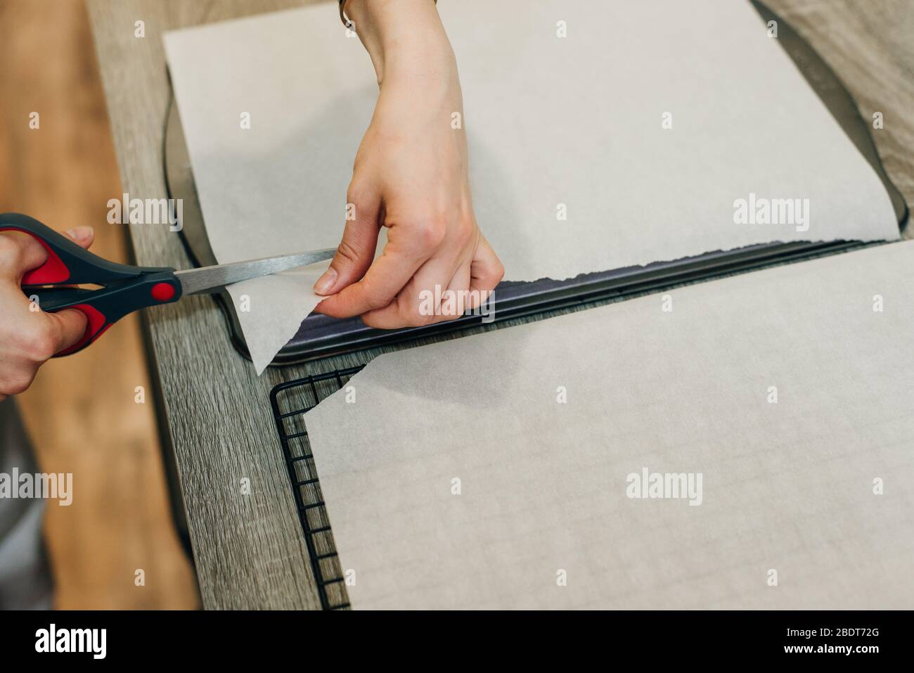 Hand holding up a sheet of baking paper and cut using a pair of ...