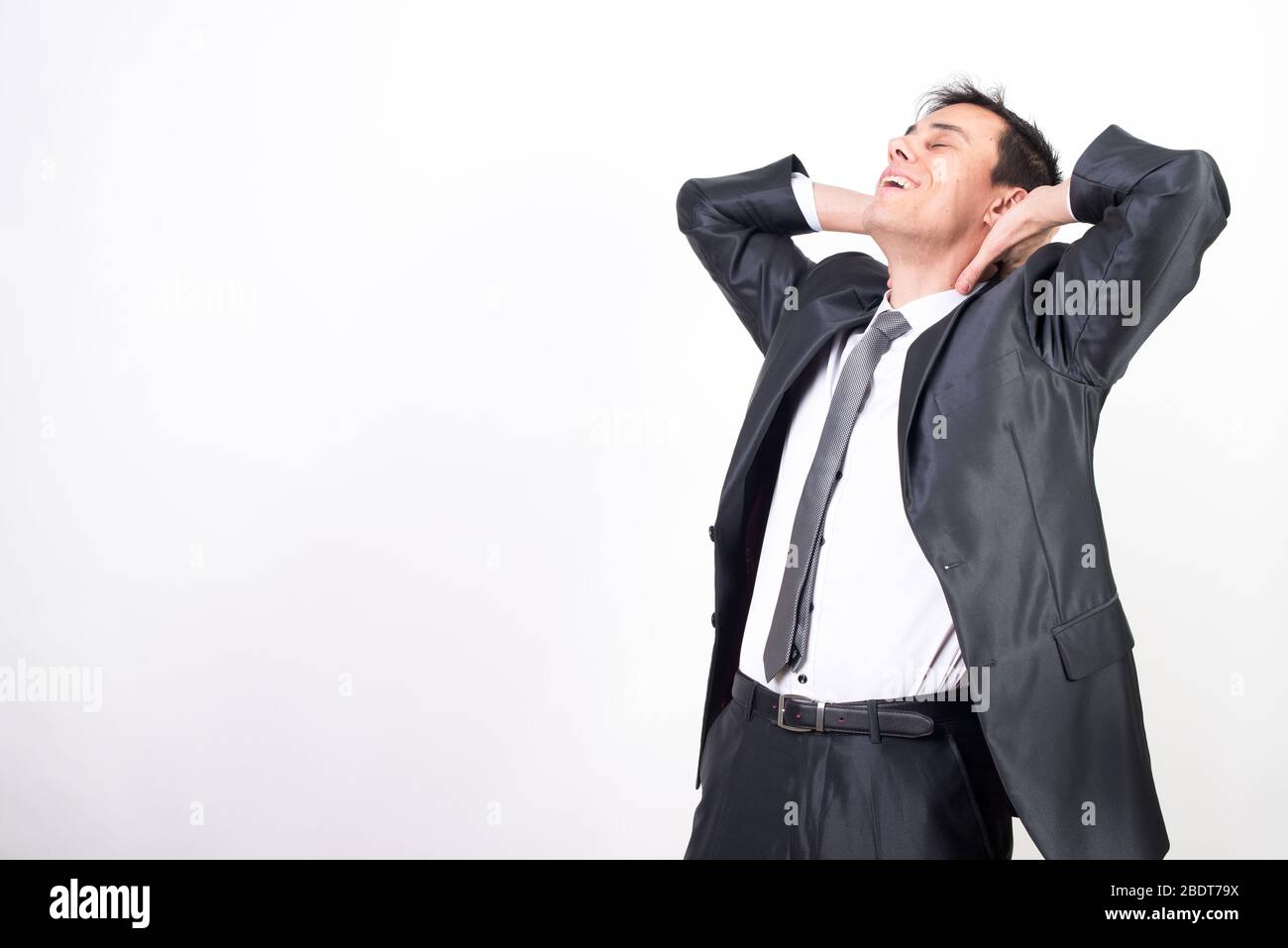 Relaxed man in suit leaning back with his hands on the back of his neck ...