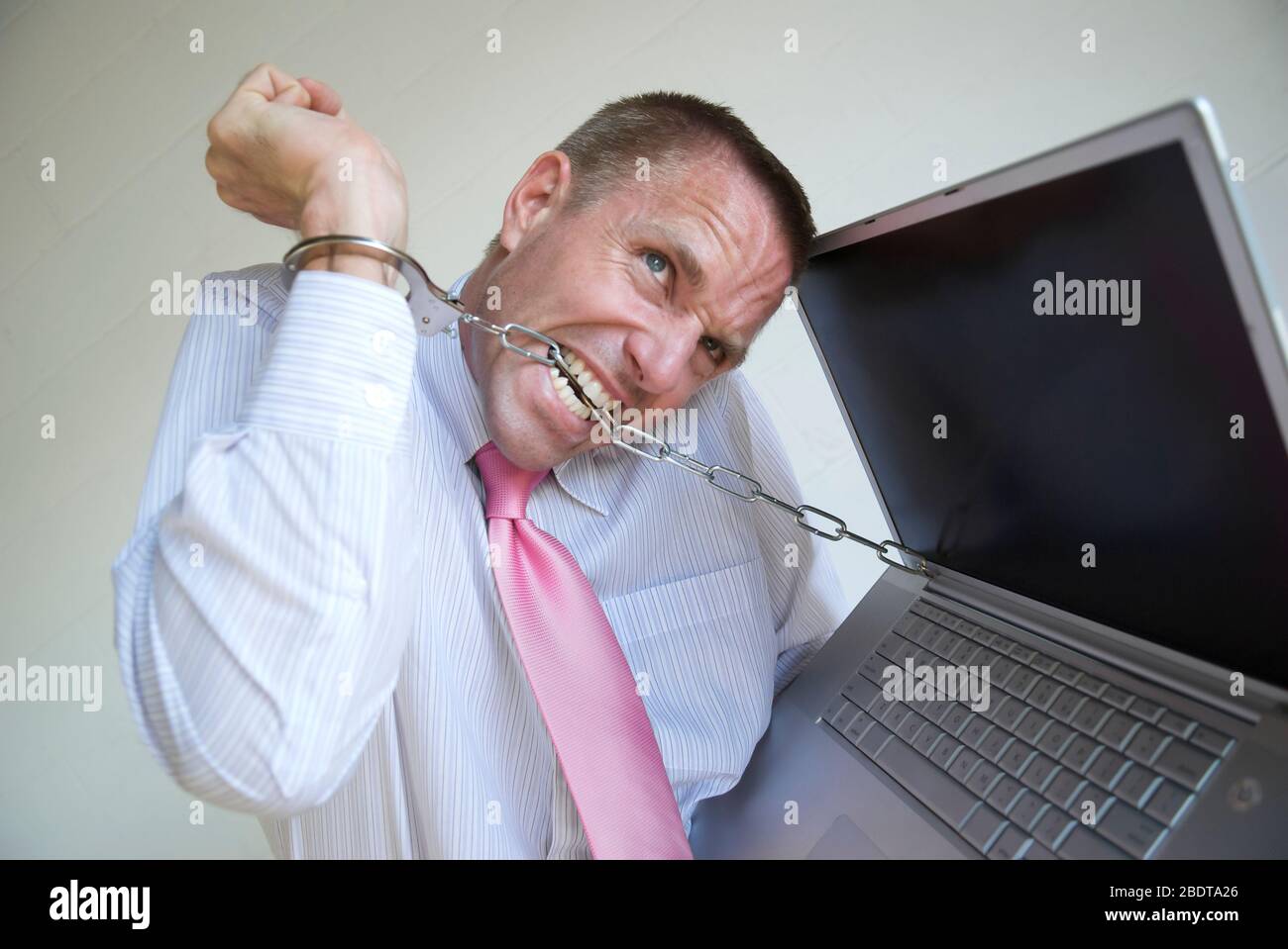 Stressed businessman handcuffed to his laptop computer trying to chew ...