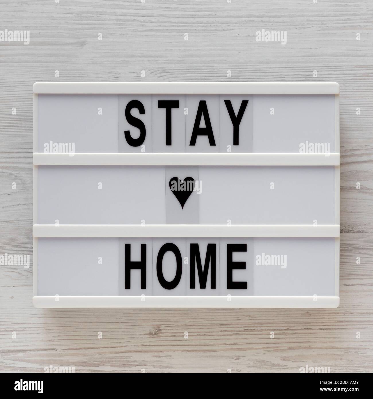 'Stay home' words on a lightbox on a white wooden background, top view ...