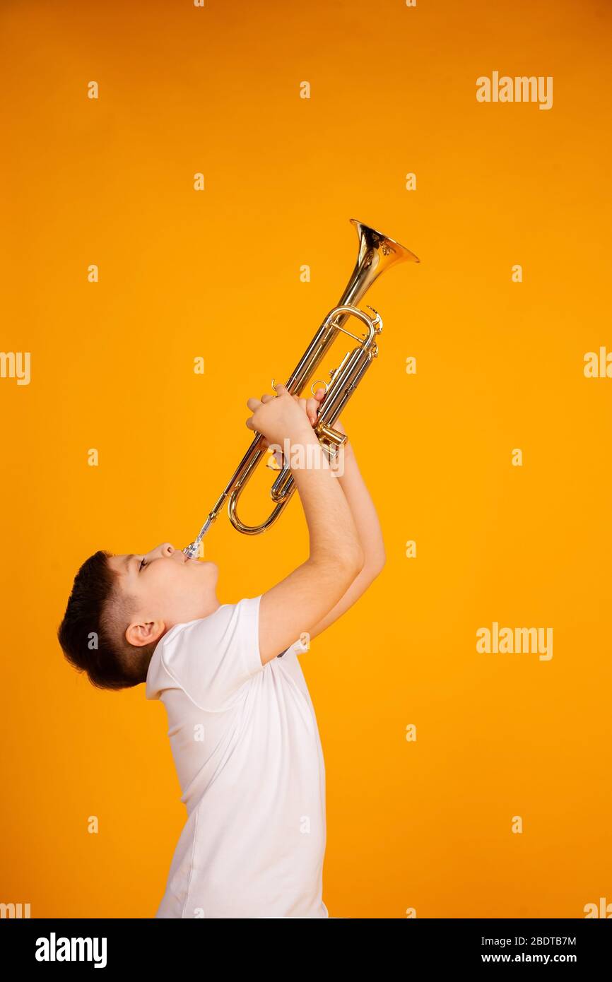 A boy plays the trumpet. A handsome teenager boy in a white T-shirt ...