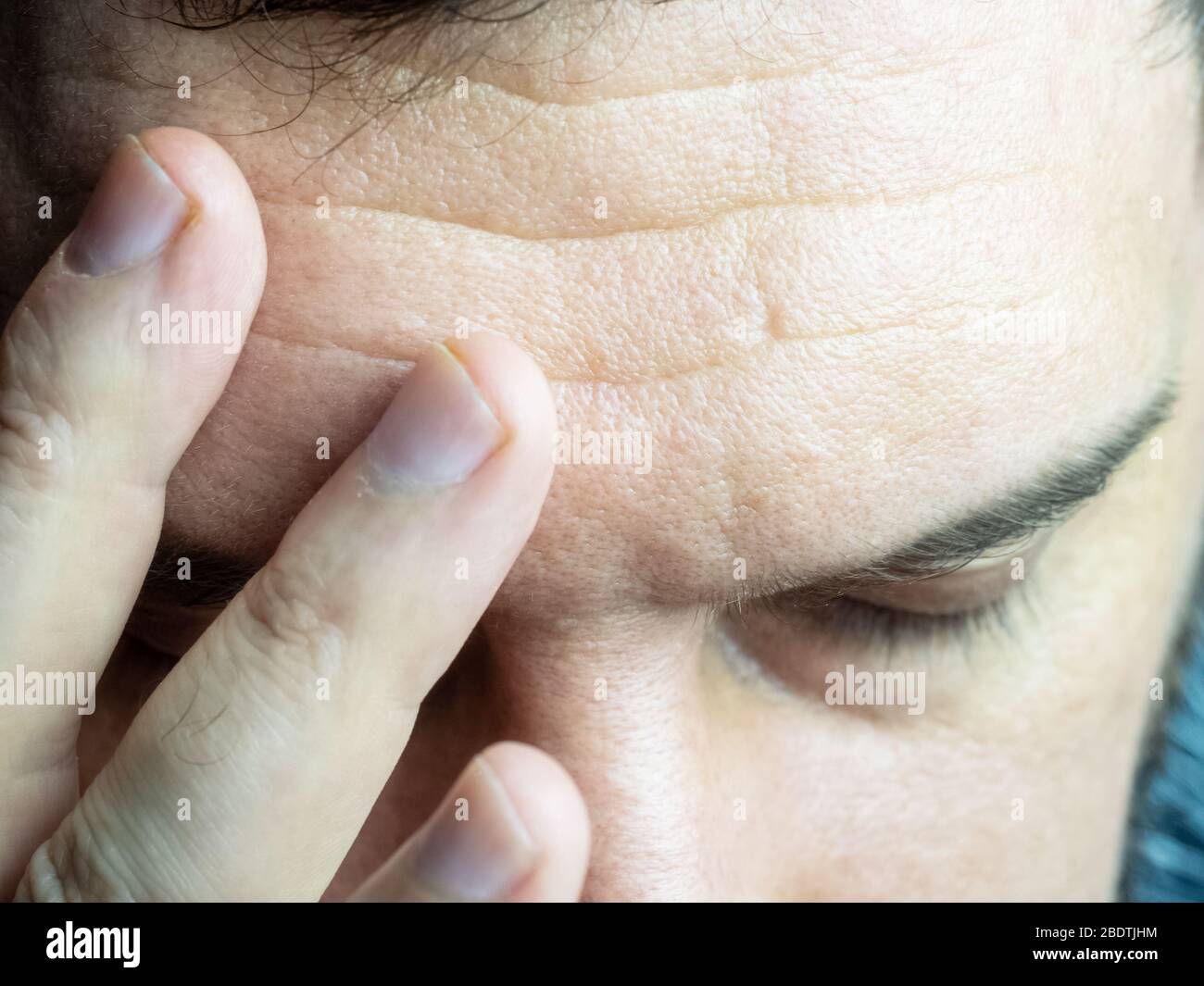 A close-up photo of a man leaning his fingers to his forehead, closing ...