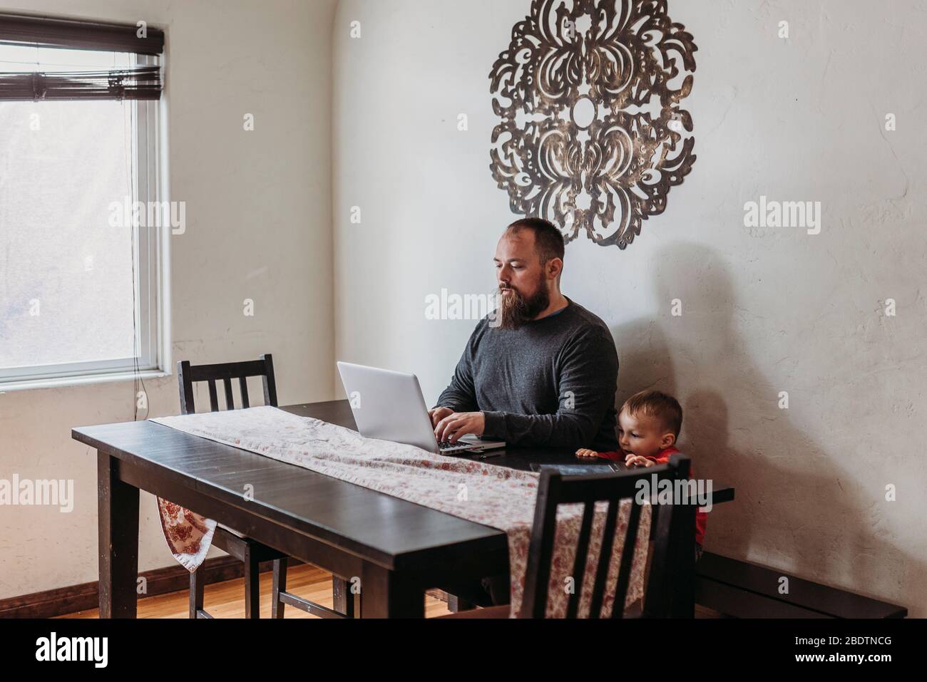 Wide view of father trying to work from home with toddler standing ...