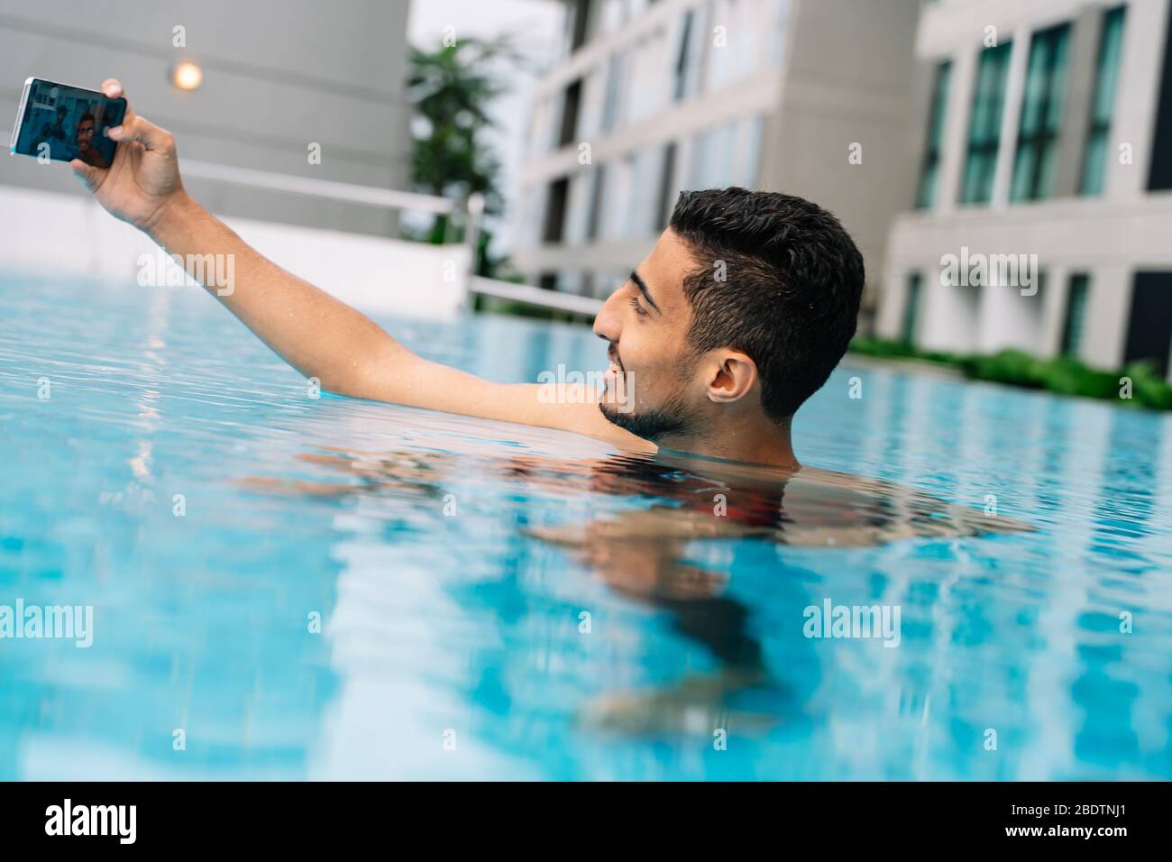 Young man making a selfie inside a pool with his friends and surrounded ...